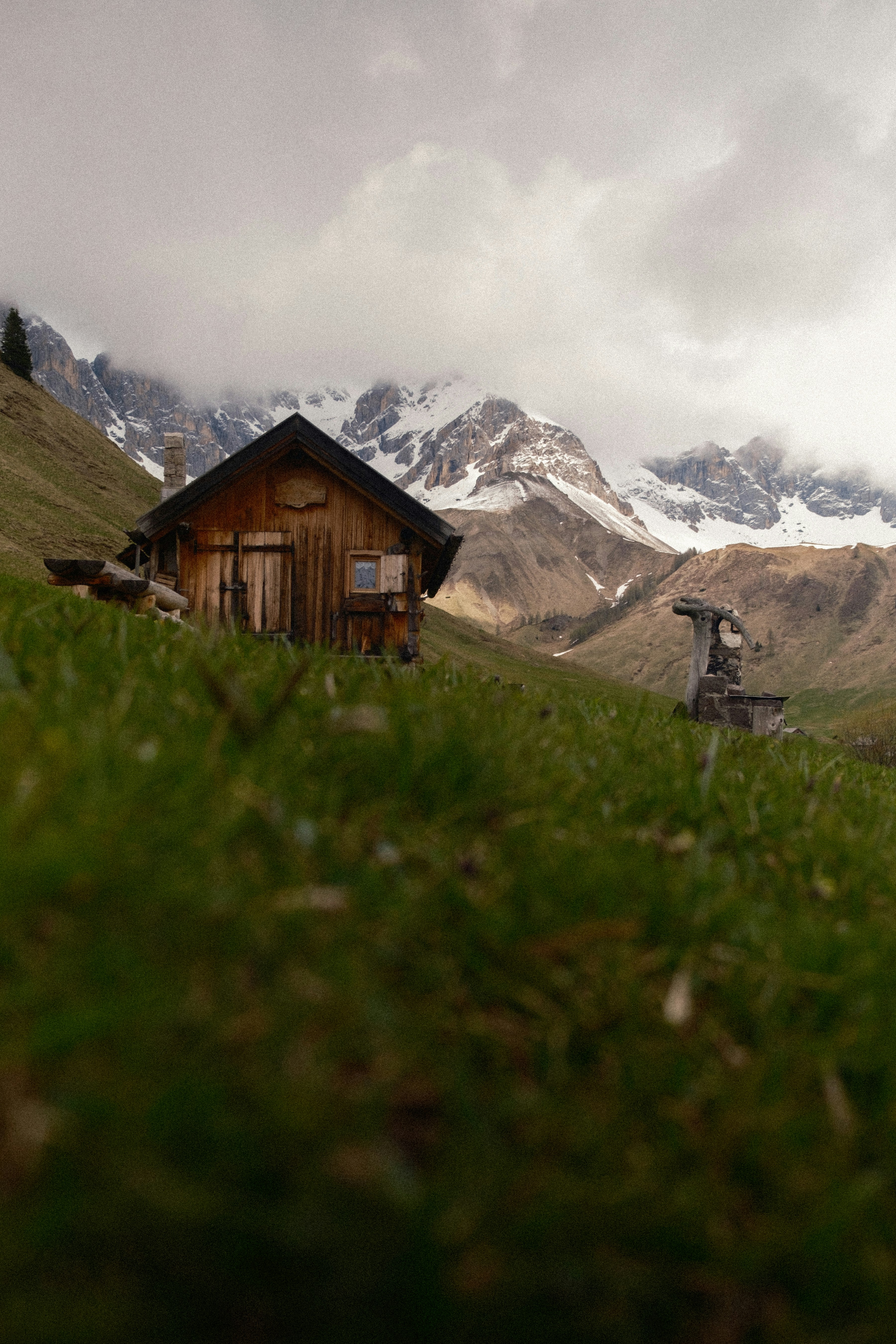 Alpine Refuge: A Wooden Cabin Nestled on a Green Slope Beneath Snowy Peaks