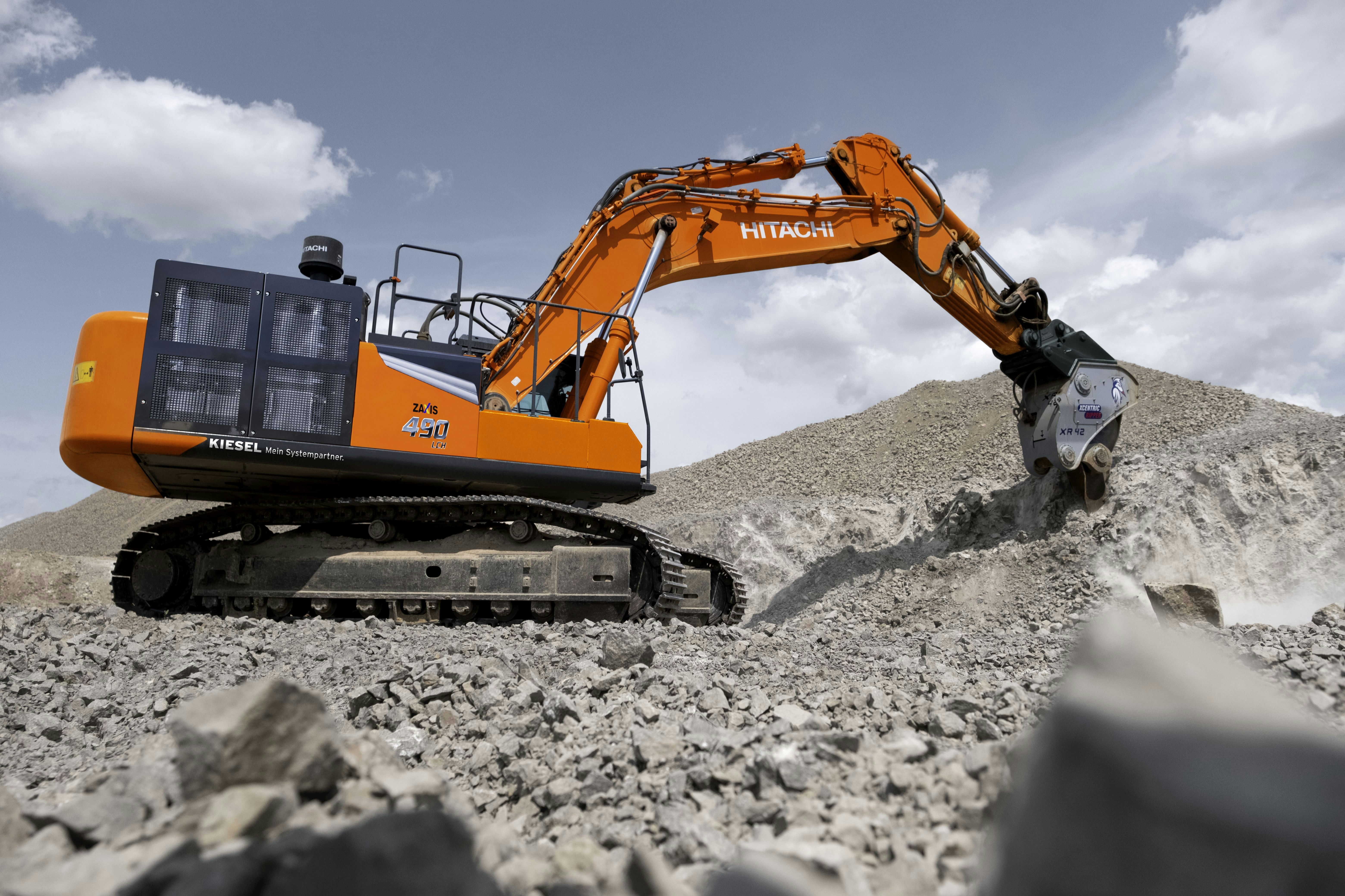 An orange excavator digging through a pile of rocks photo – Free Brown ...
