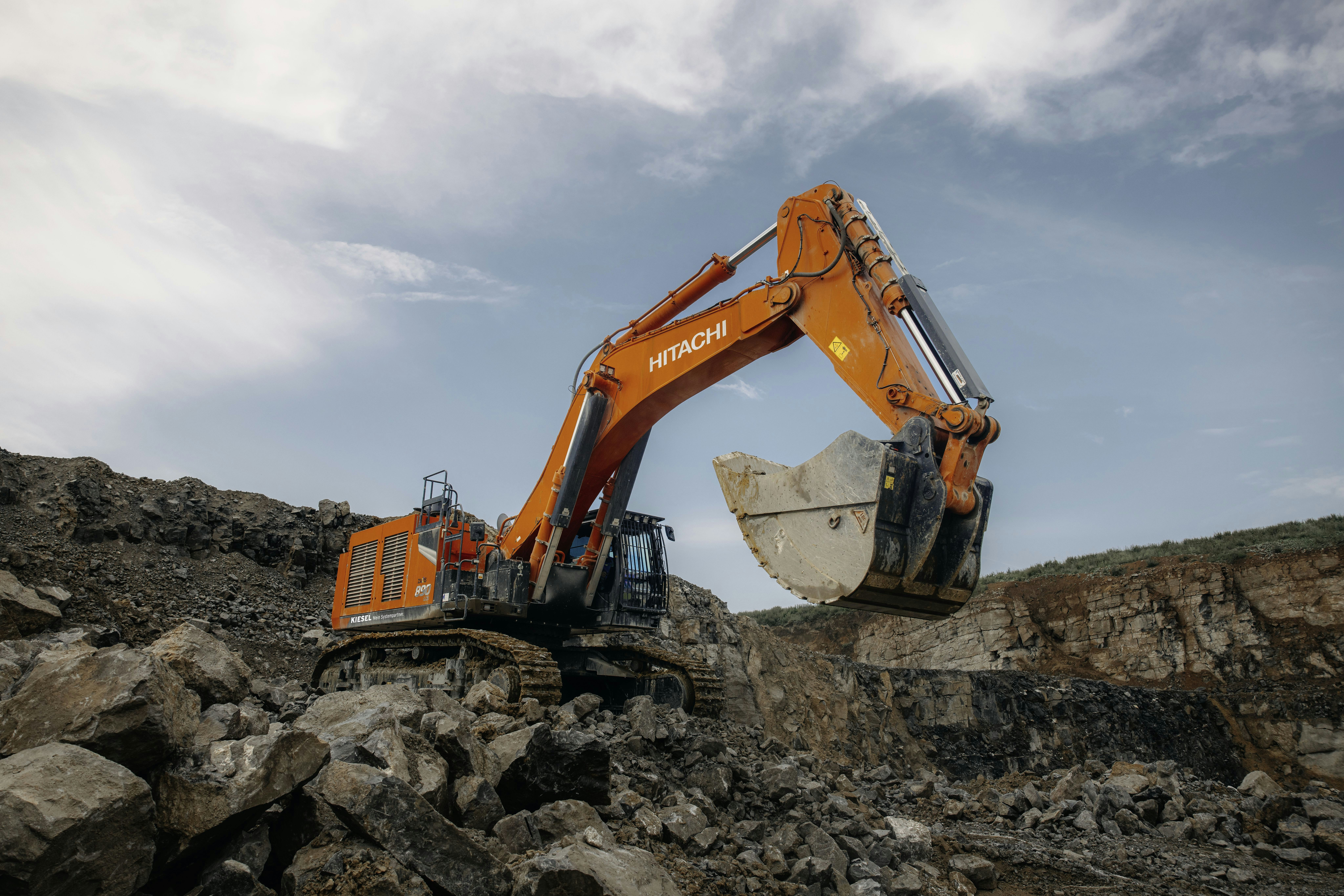 An orange excavator digging through a pile of rocks photo – Free Bagger ...