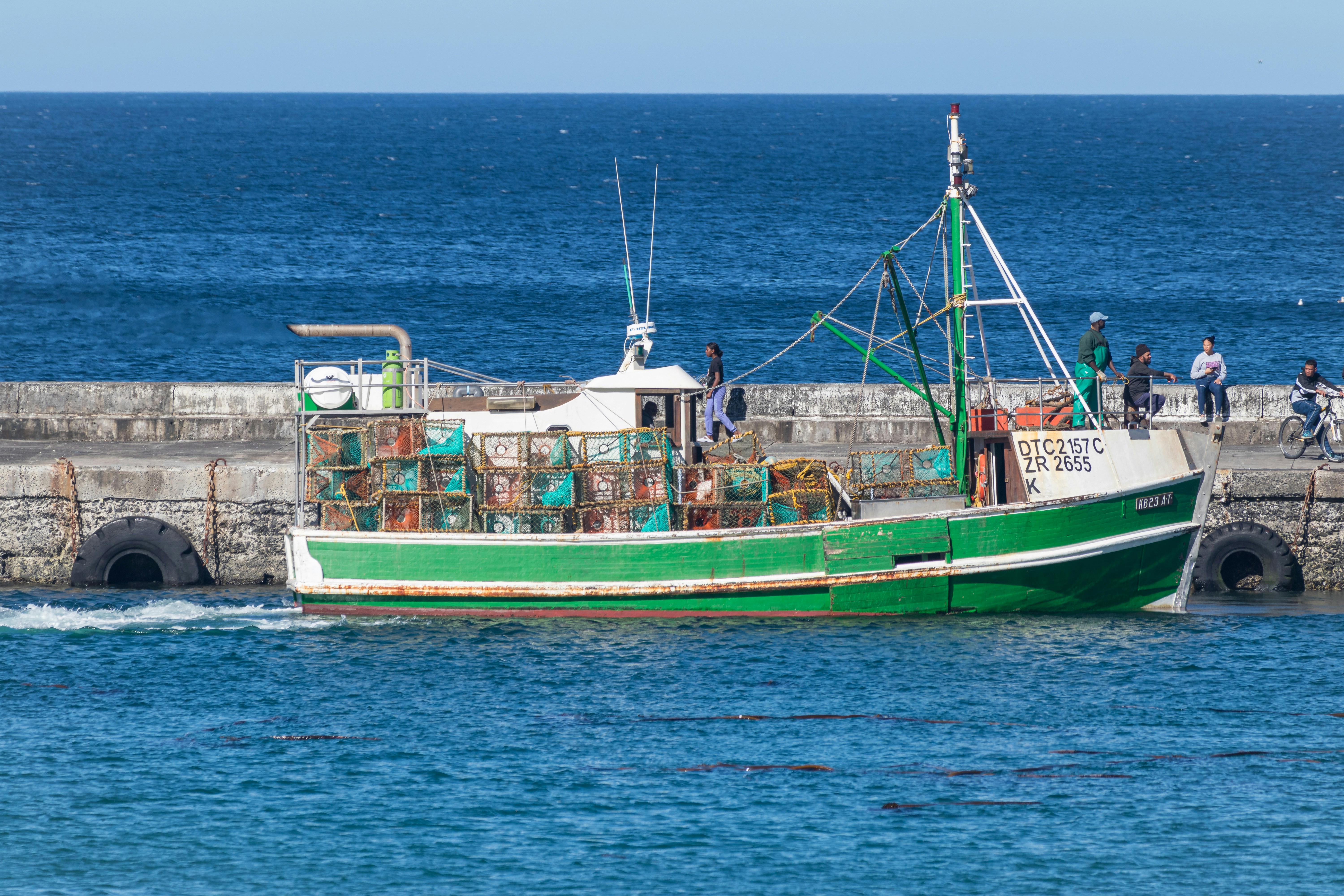Green-hulled fishing boat at a sunlit harbor breakwater