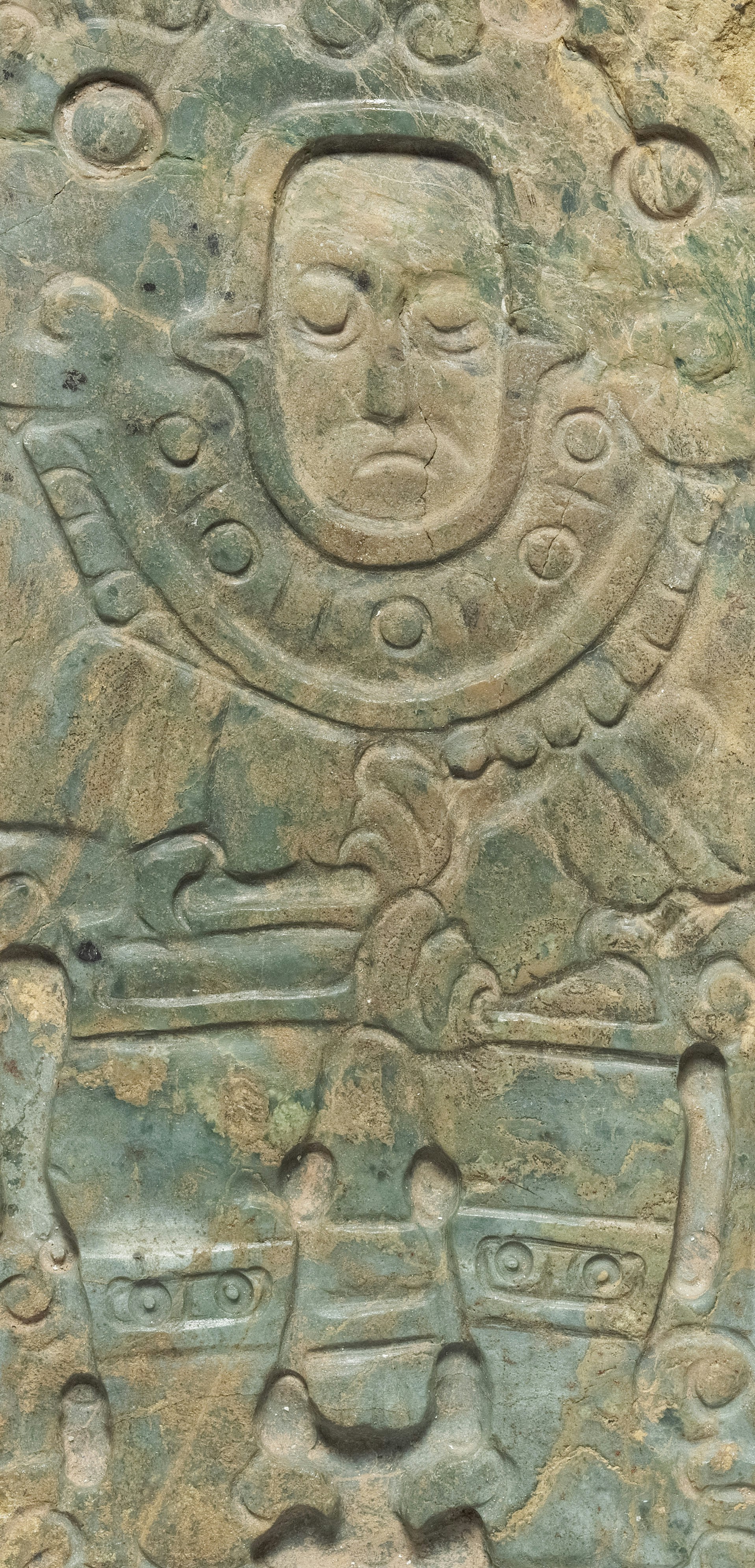 Intricate stone carving depicting a solemn figure adorned with circular motifs. The craftsmanship highlights the artistry of ancient cultures.