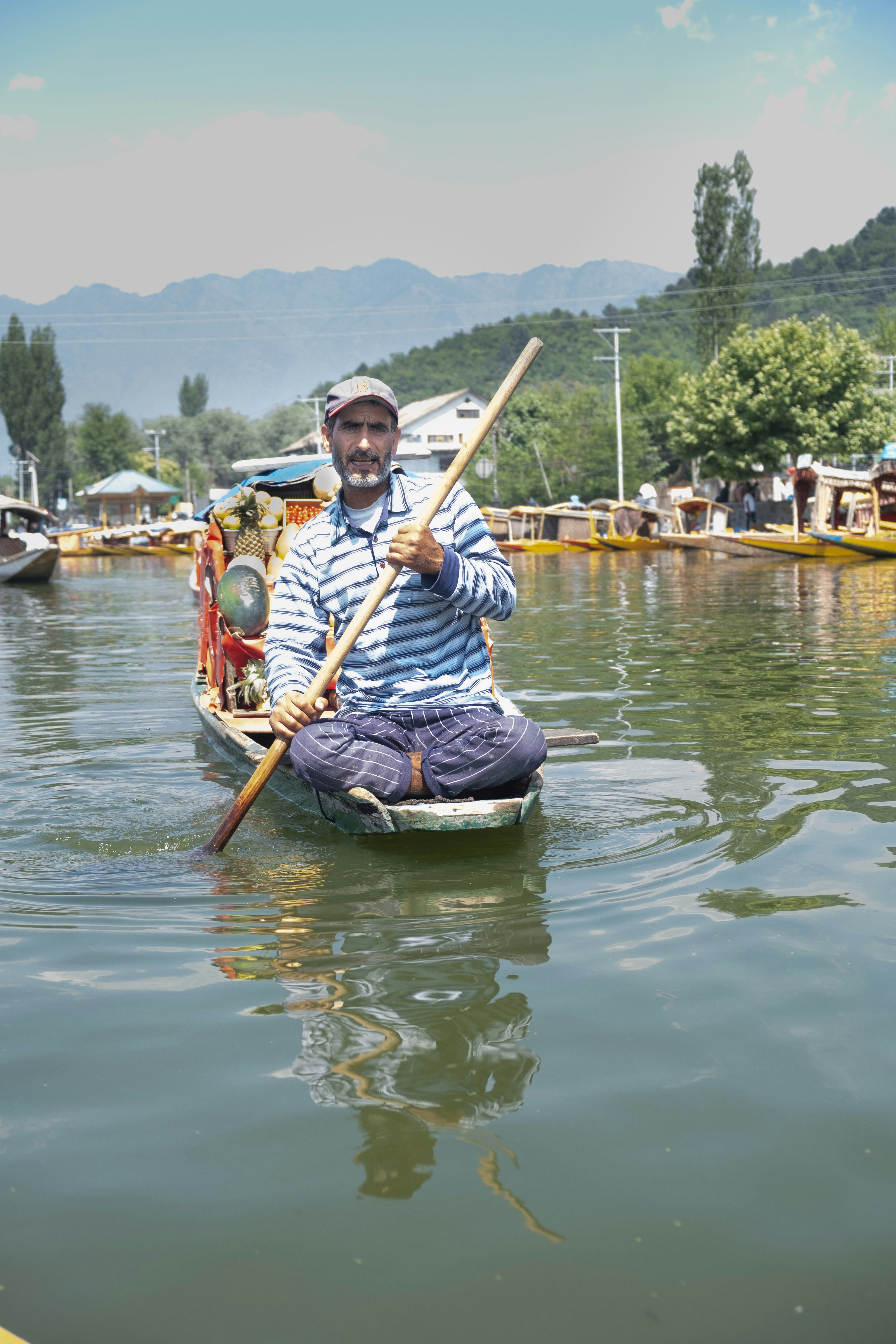 Floating Market Canal: A Lone Paddler Navigates Quiet Waters beneath Mountain Peaks