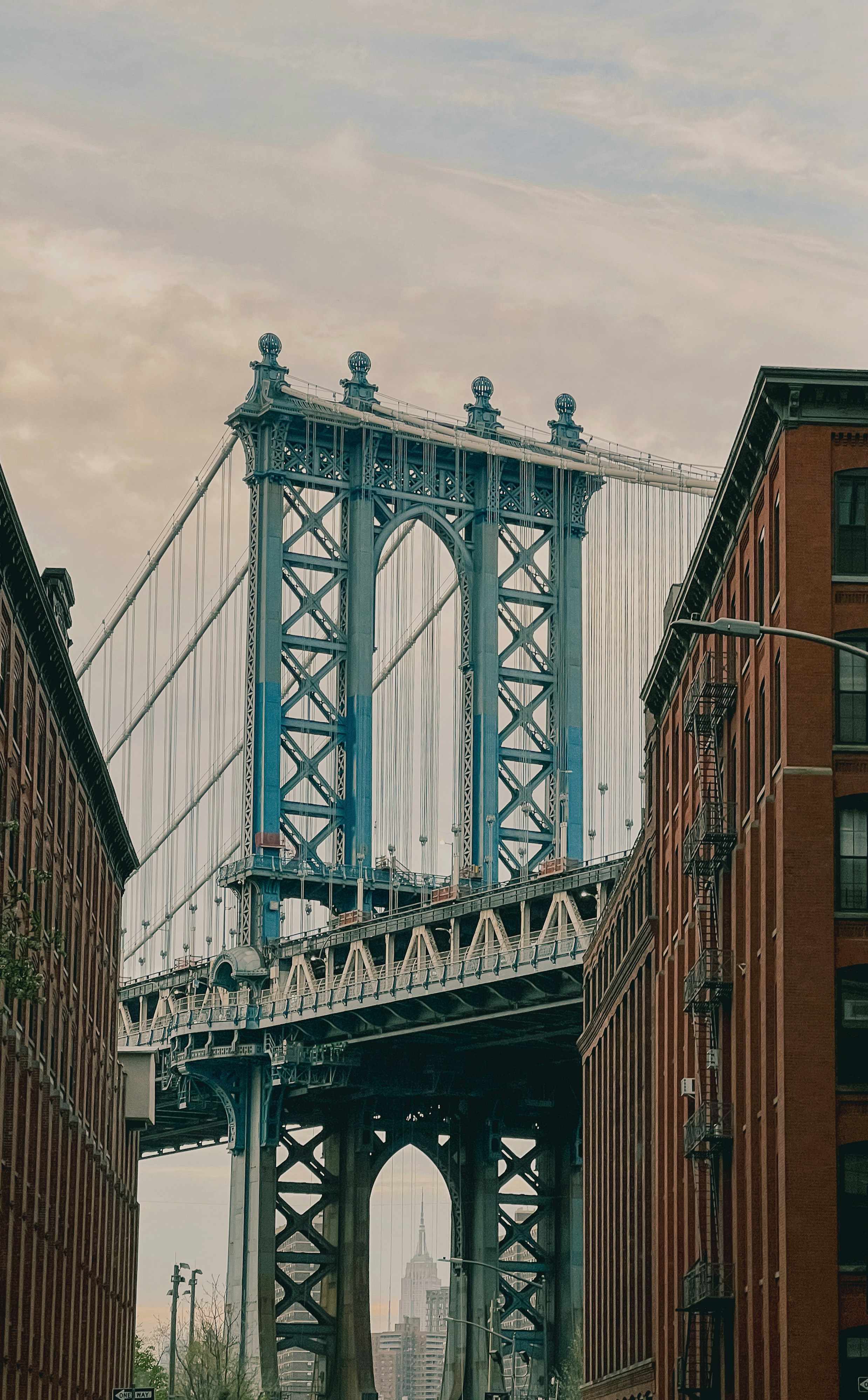 The Manhattan Bridge framed by historic red-brick buildings, showcasing urban architecture against a cloudy sky.