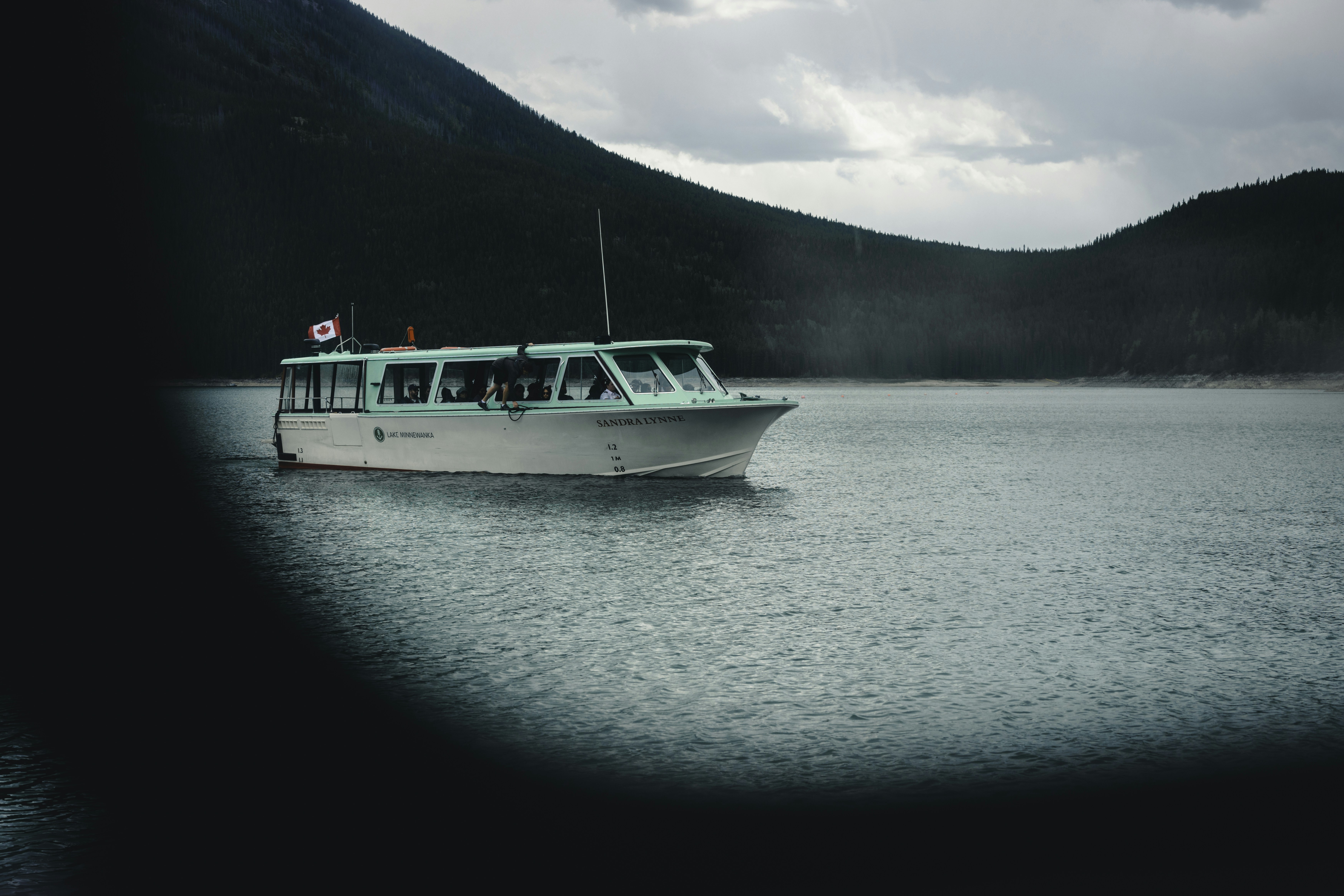 White Tour Boat Slicing Through a Calm Mountain Lake, Framed by a Dark Circular Vignette