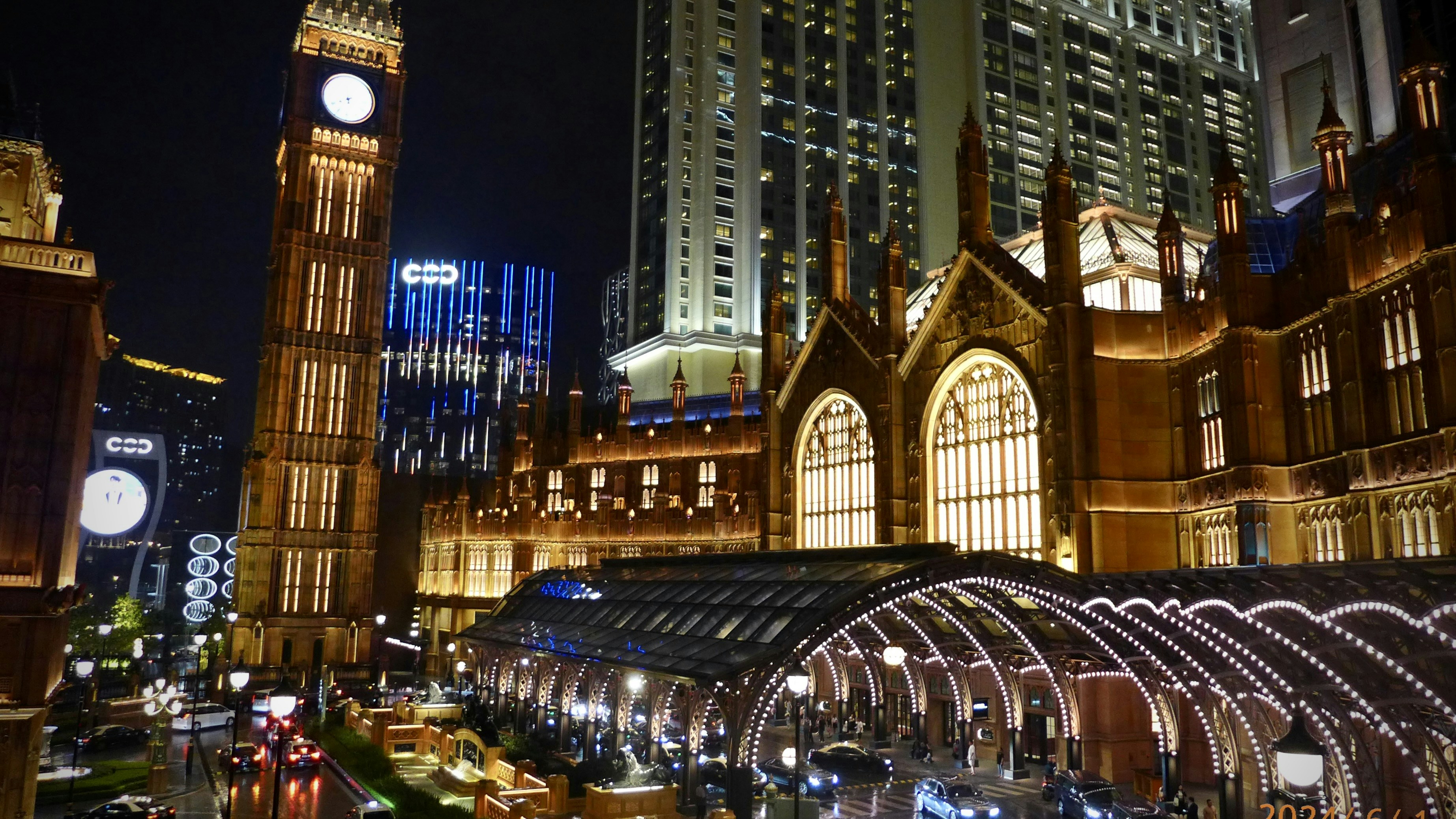 Historic clock tower and modern architecture illuminated at night, showcasing the contrast between tradition and contemporary design.