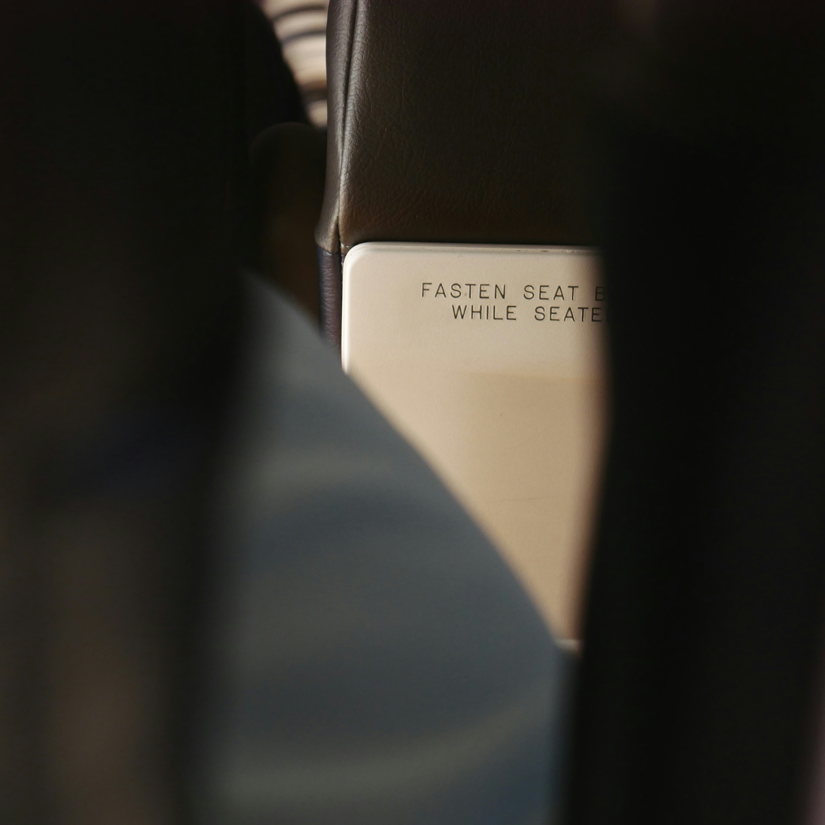 Seatbelt warning sign affixed to an airplane seat, emphasizing passenger safety during flight.