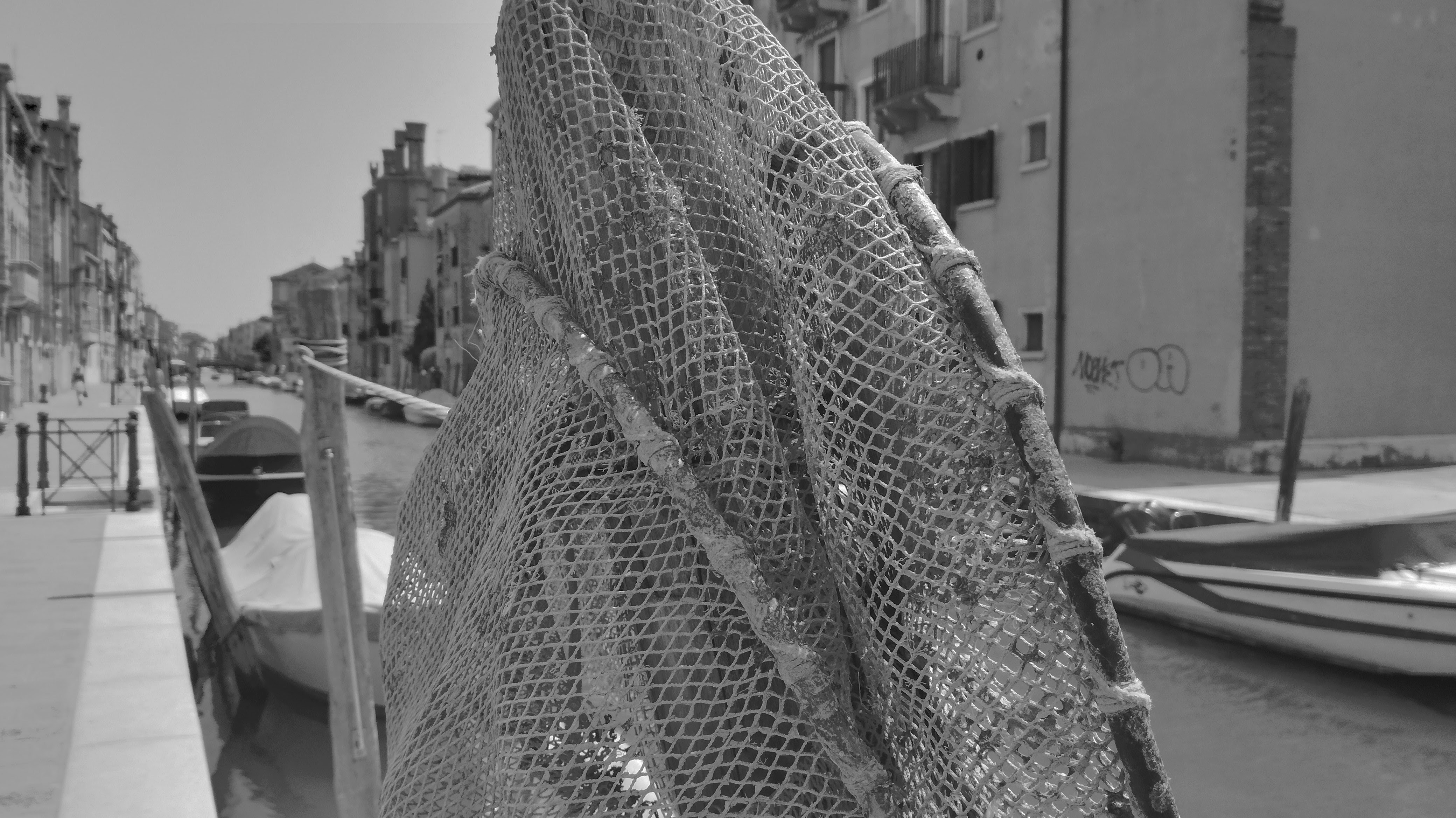 Black and white composition of a boat with a textured cover in a narrow canal lined with historic buildings.