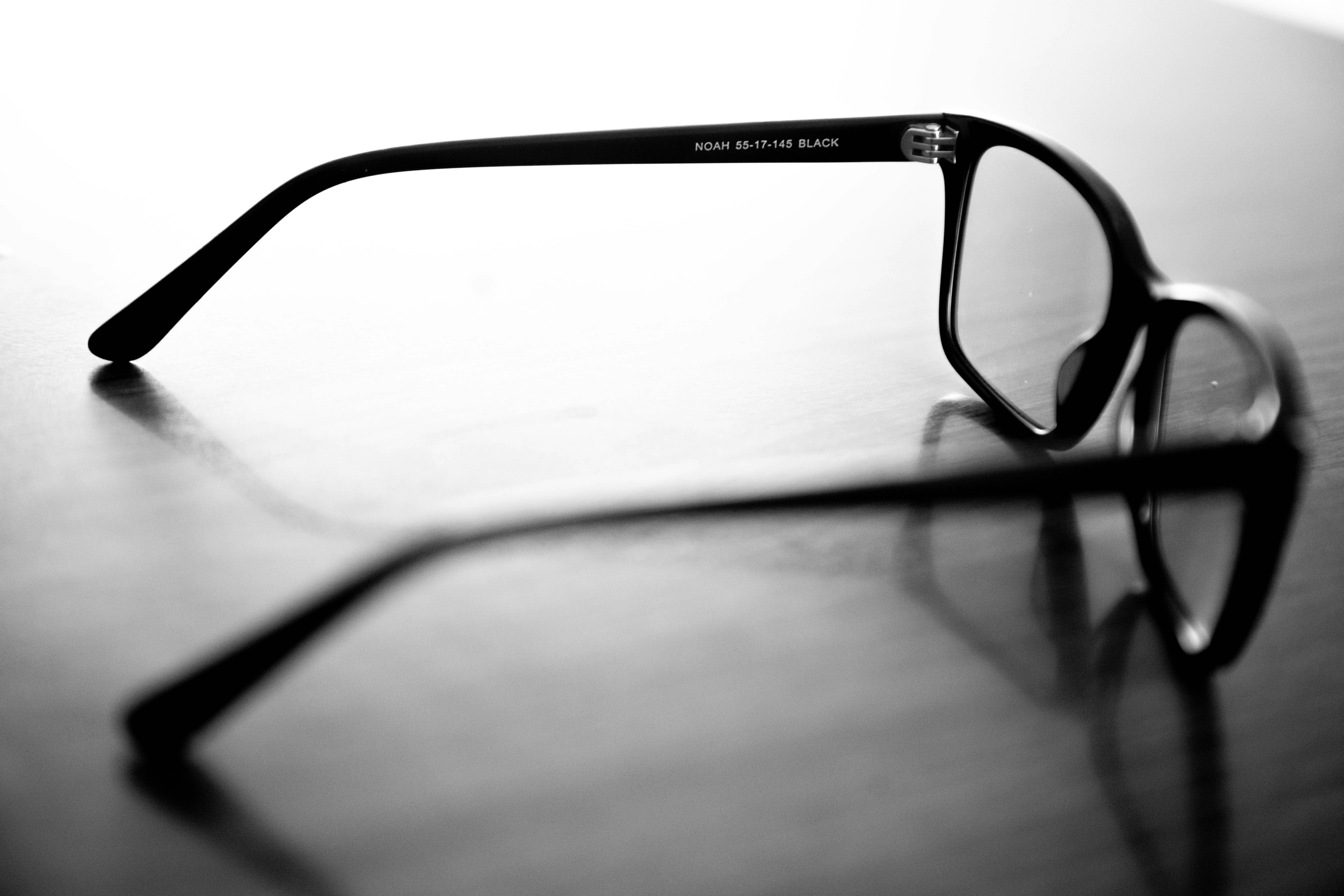 Black rectangle eyeglasses resting on a polished wooden surface, reflecting light gracefully.
