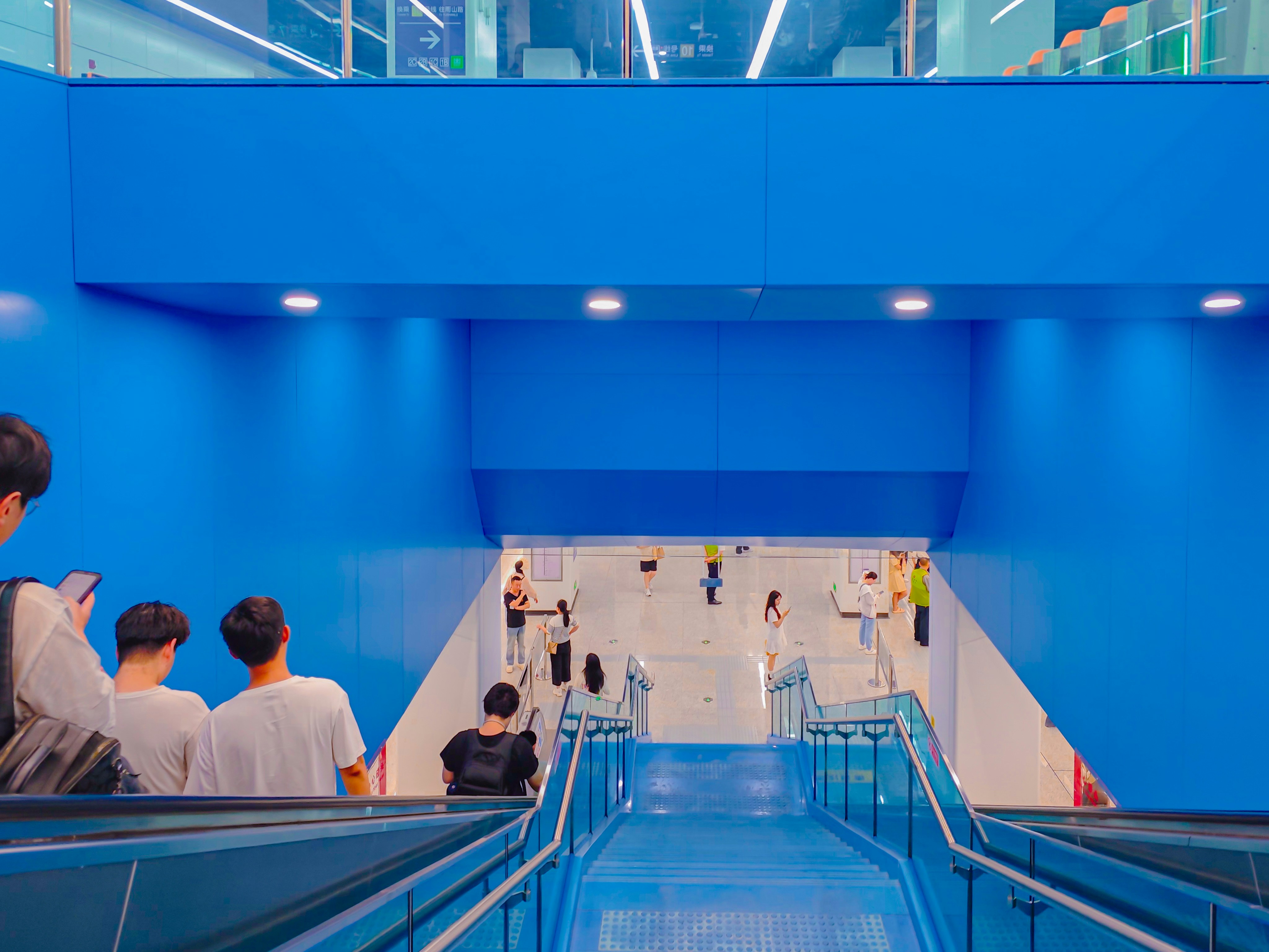 Blue Threshold: People Descend into a Neon-Illuminated Transit Hall