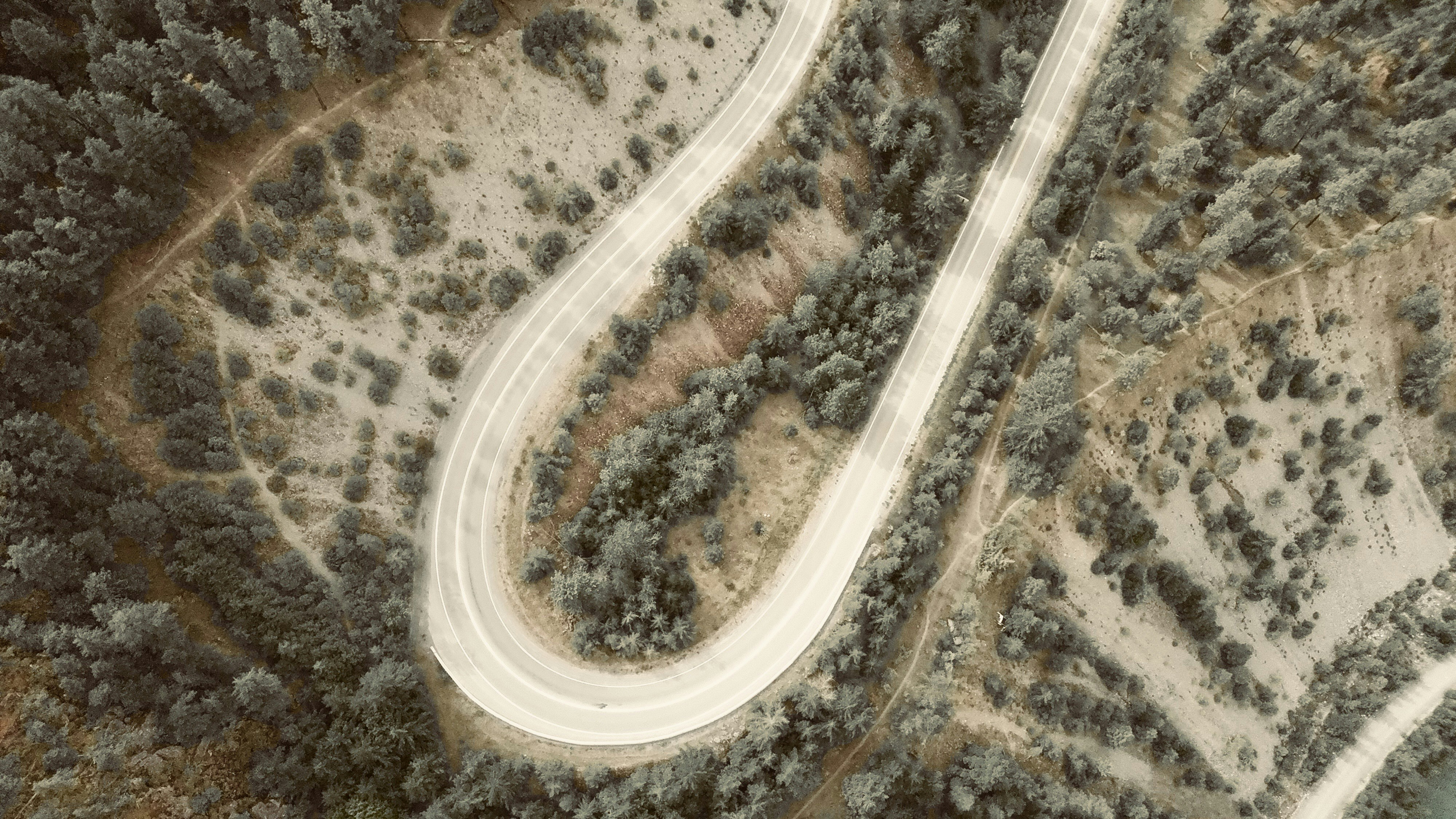 Aerial drone photograph capturing a winding desert road looping through scrub and arid hills, revealing sculpted textures and shadows along the slope.