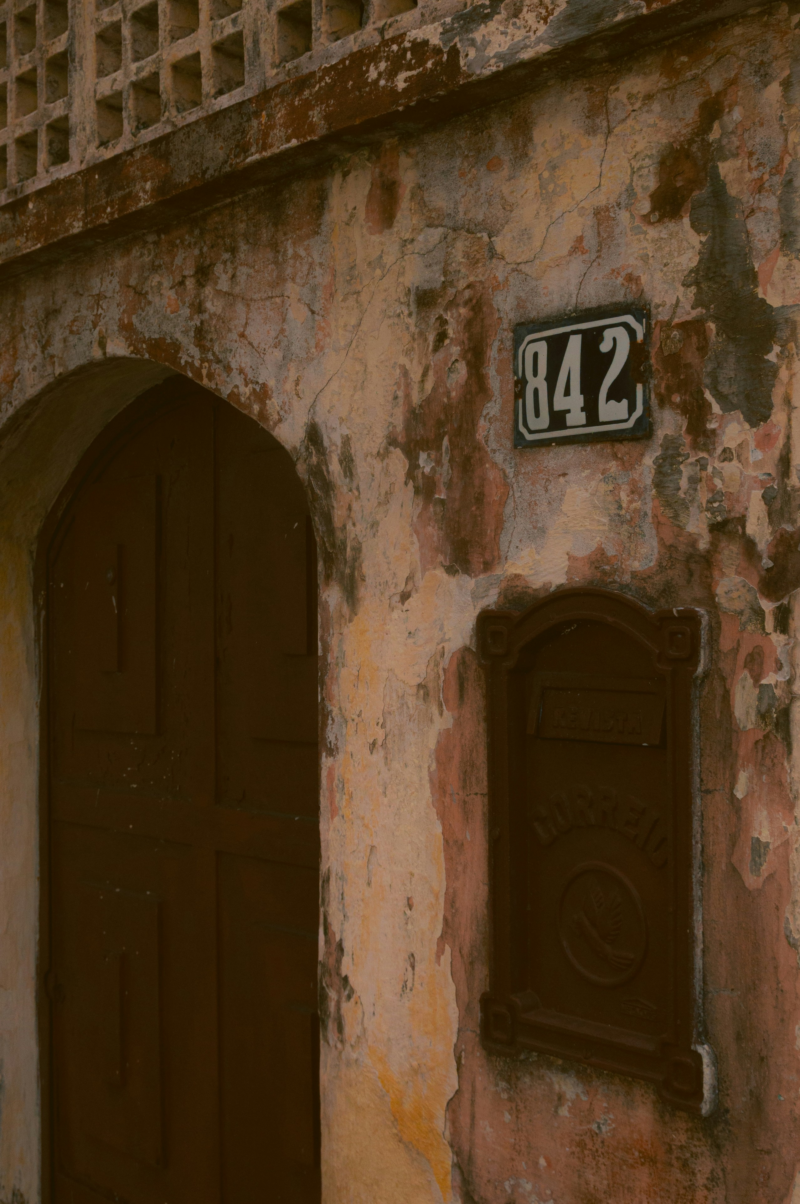 Weathered doorway under a rusted facade with a numeric plaque 84.2