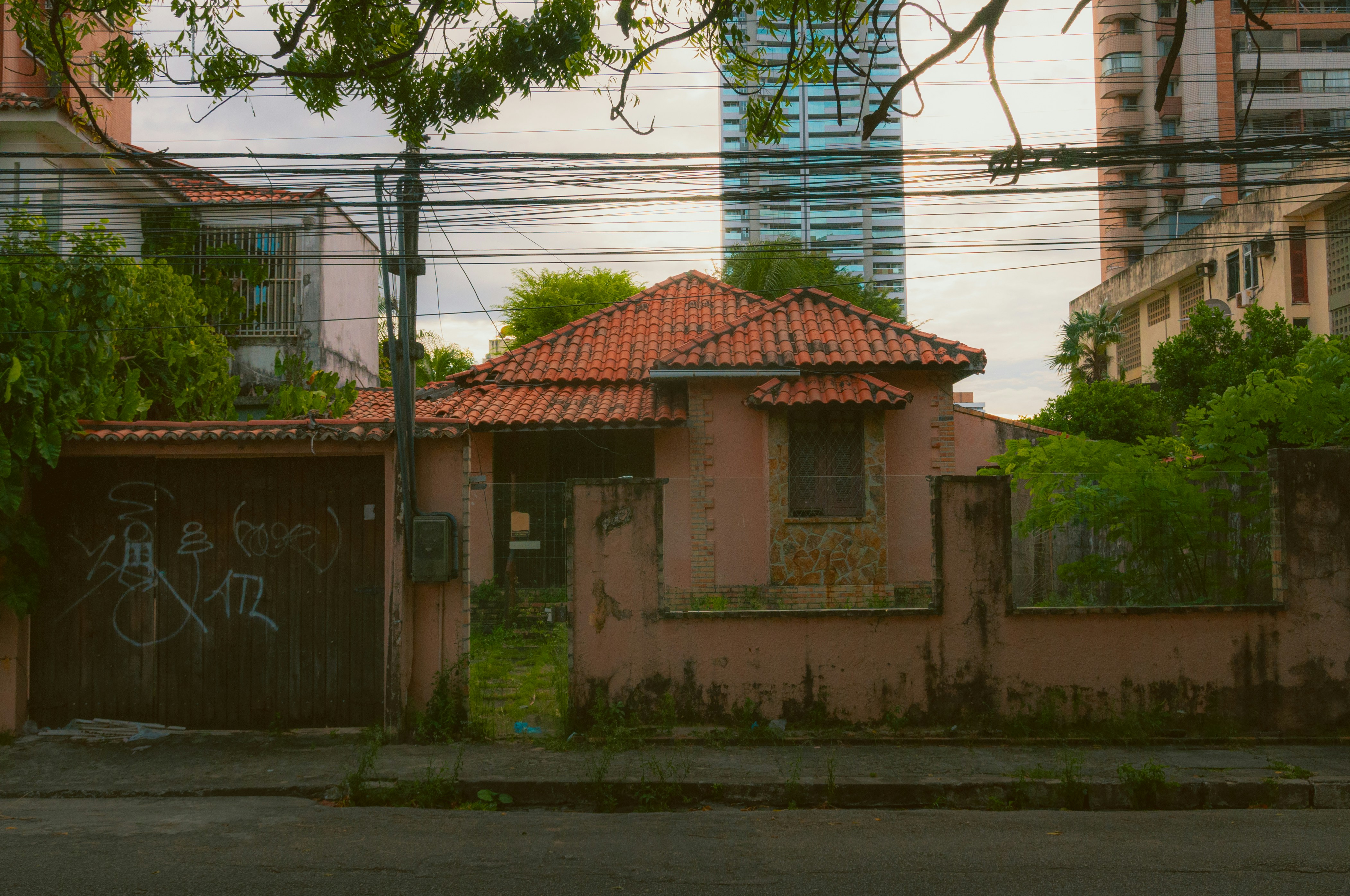 Pink-Tiled House Anchored Between Graffiti Gates and Urban Towers