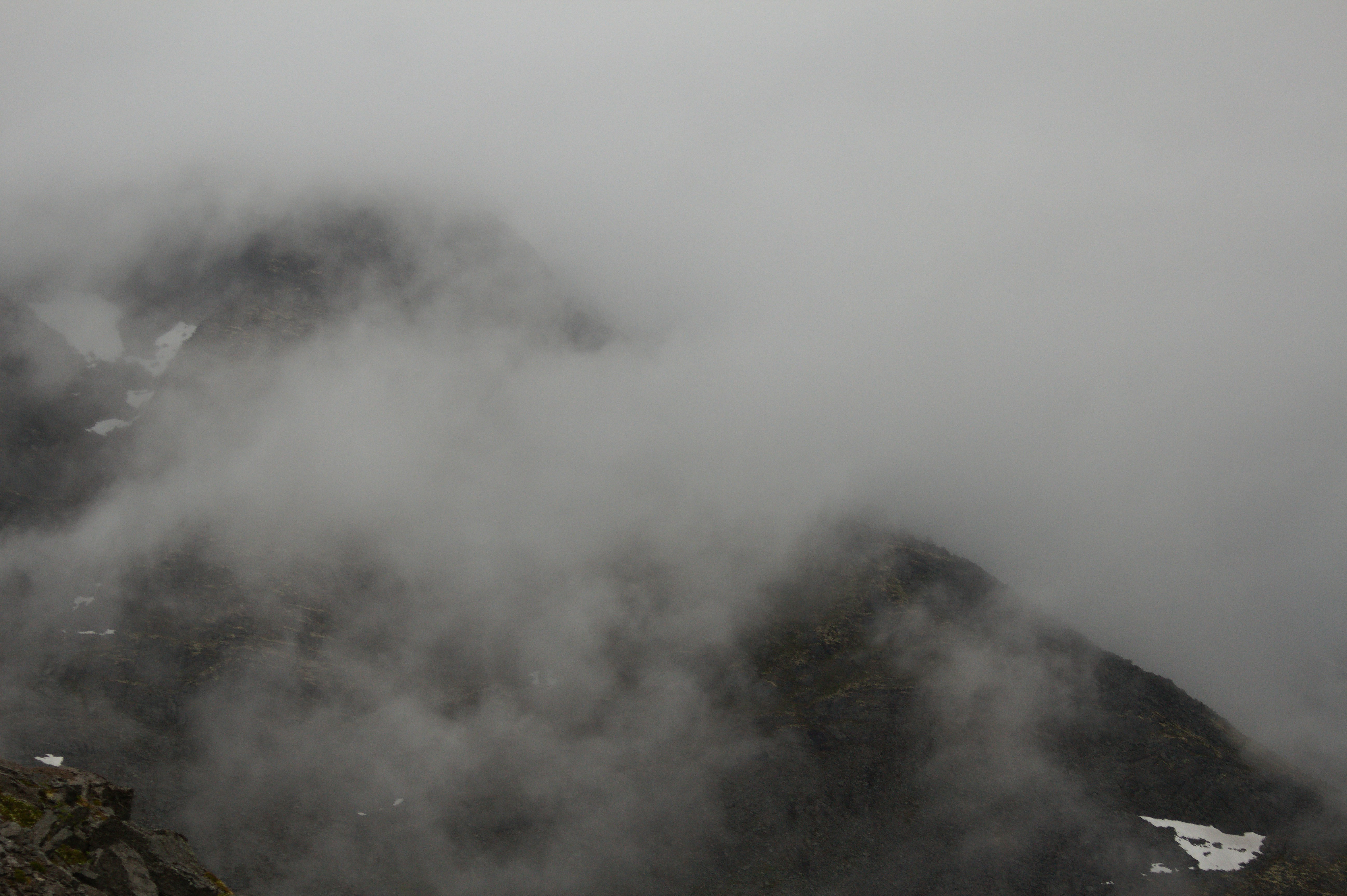 Misty mountains shrouded in thick fog, revealing hints of snow-capped peaks. The atmosphere evokes a sense of mystery and tranquility.