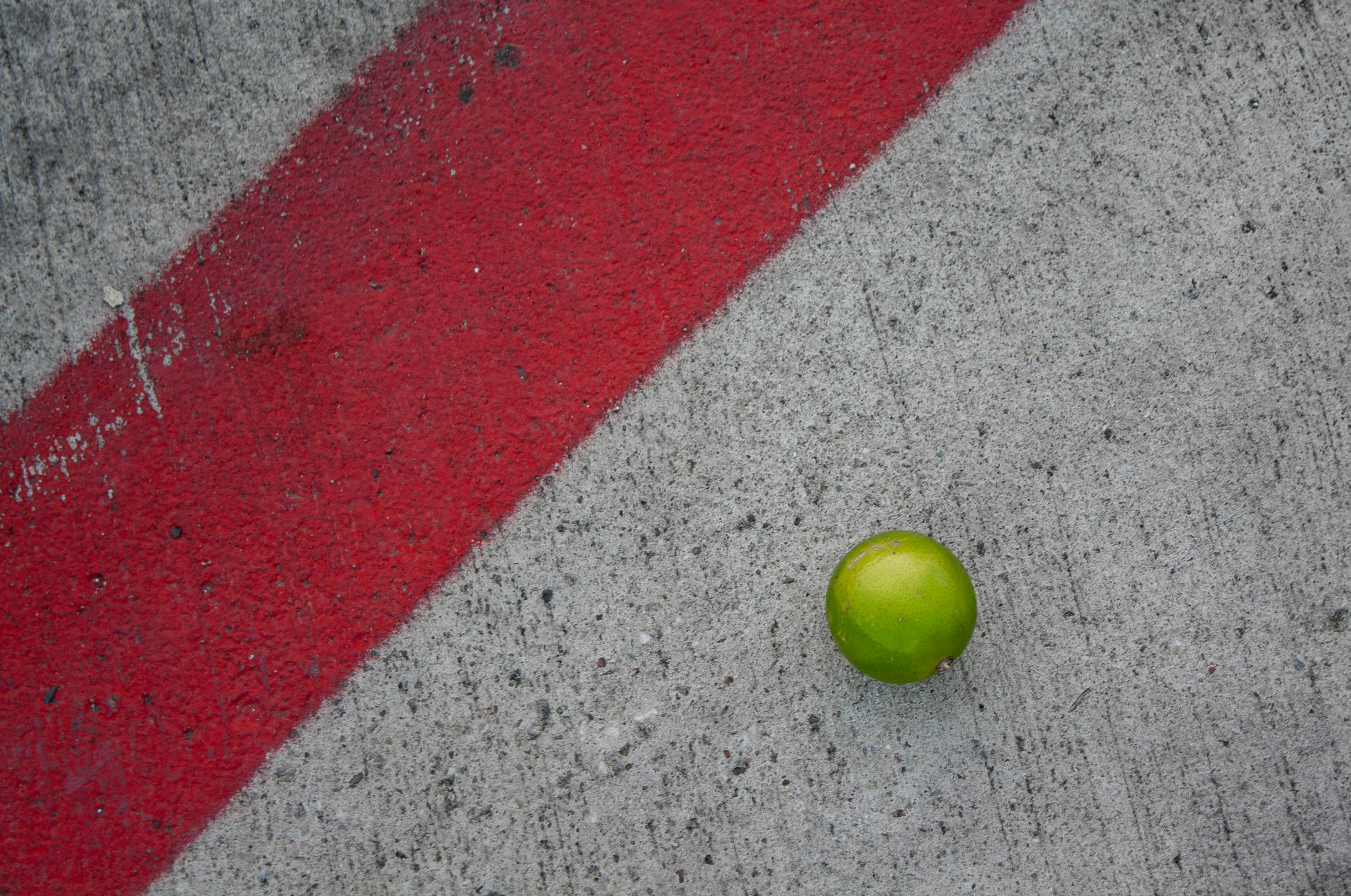 Emerald Lime on Concrete: A Minimal Moment Beneath a Crimson Diagonal Stripe