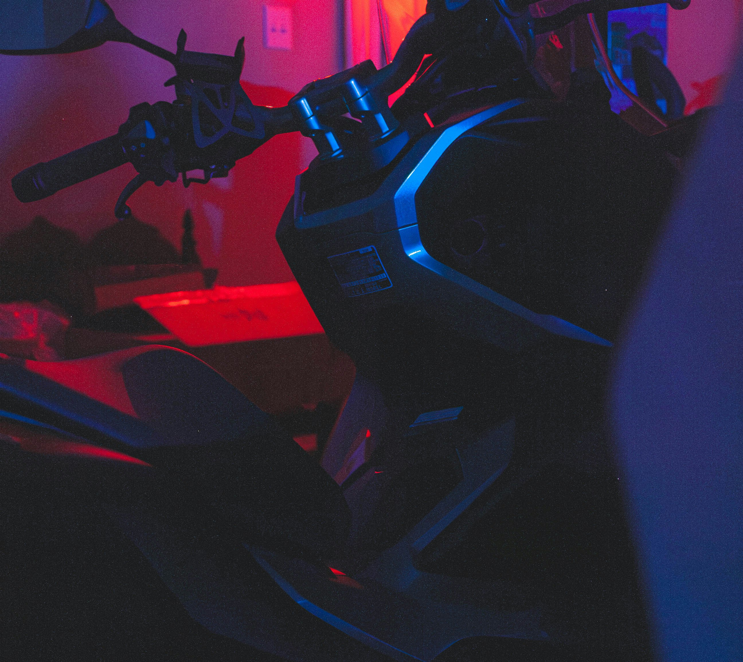 Neon-lit bike cockpit: a close-up of rider and handlebars in moody red-blue hues