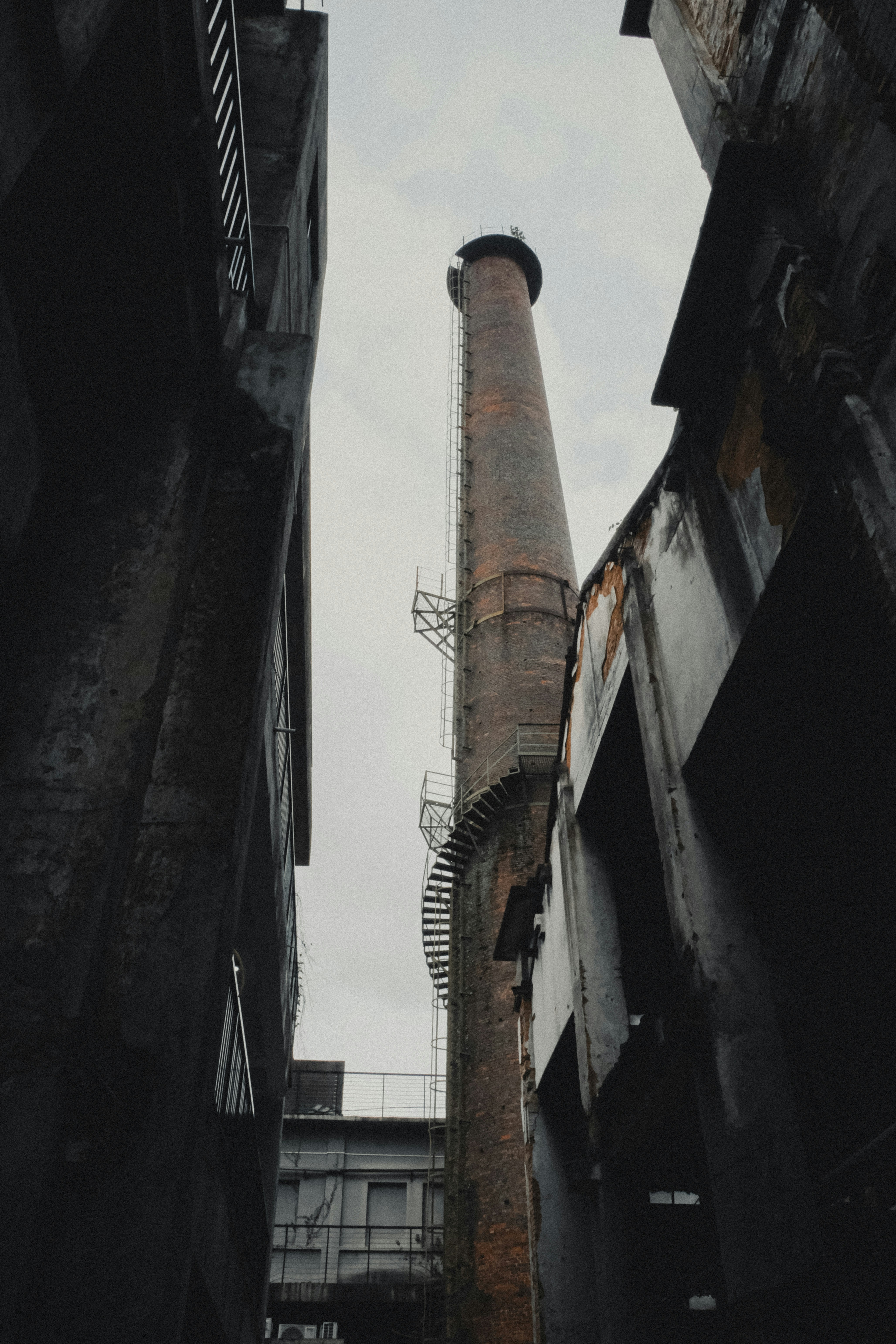 Between Shadows: A Weathered Chimney Rises in a Narrow Industrial Gap