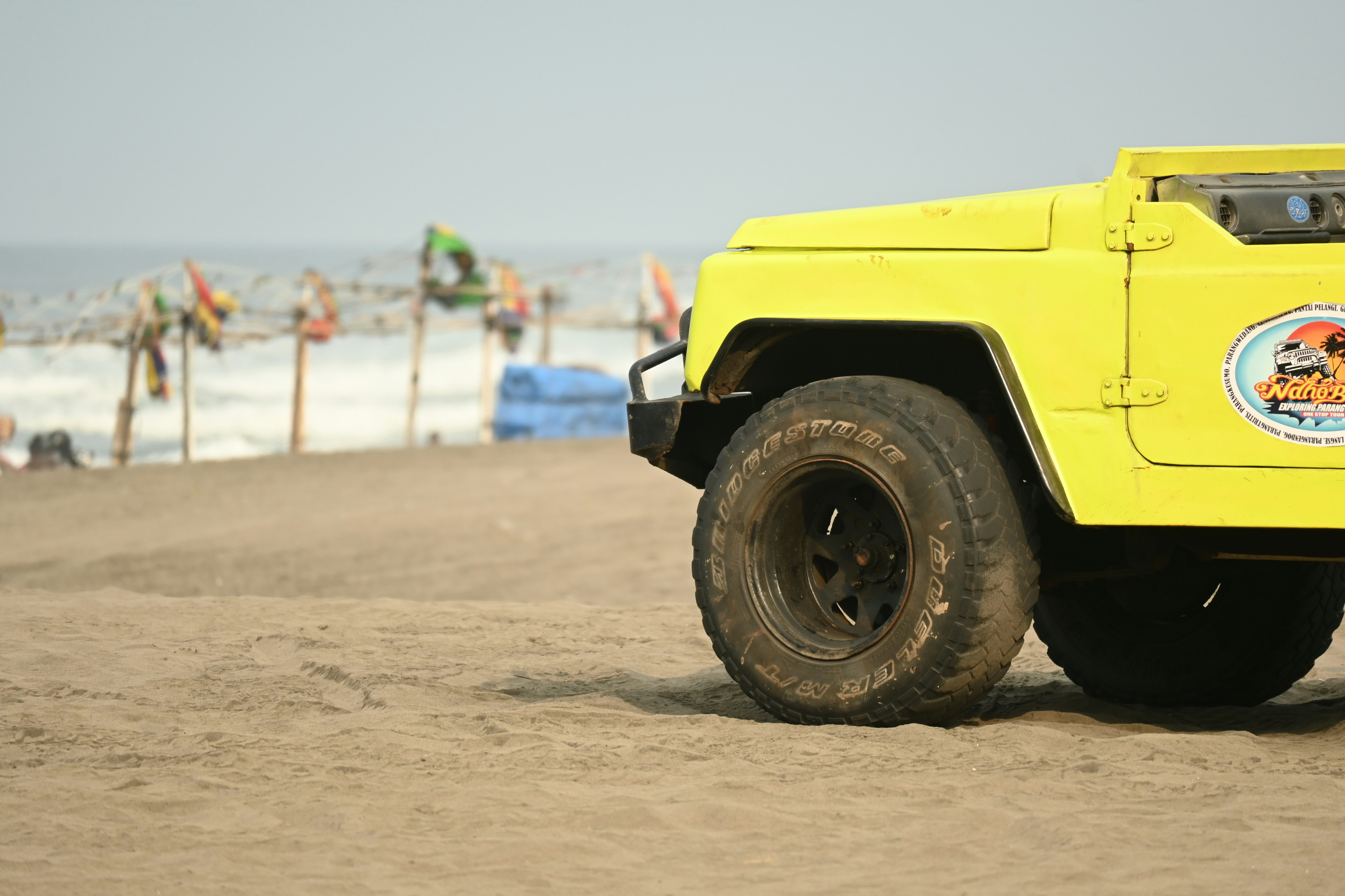 Sunlit Shoreline Stance: A Yellow Jeep Anchored by the Lapping Waves