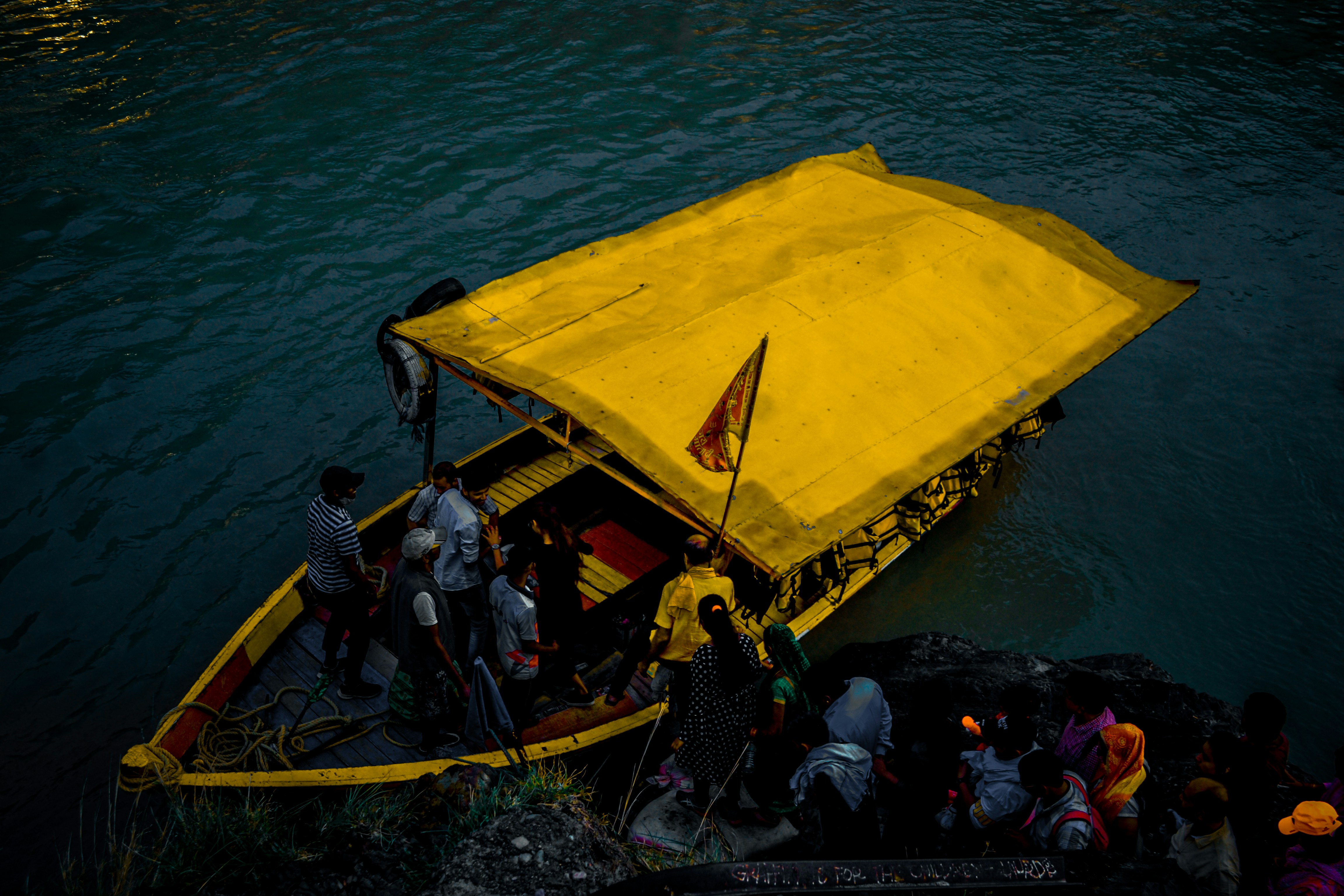 Yellow-Canopy Ferry at Dusk: Crowds Gather Along the Riverbank