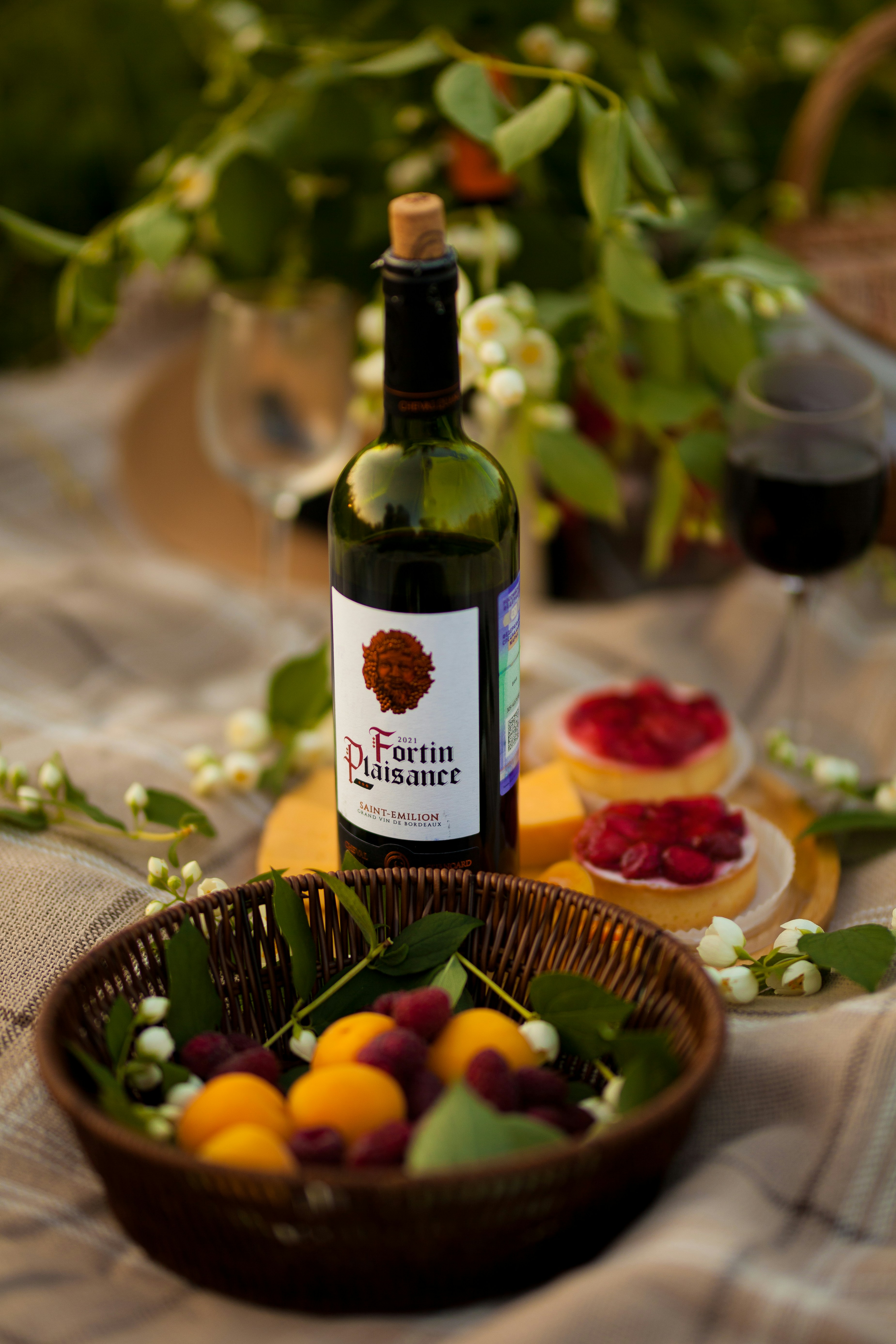 Centerpiece of Quiet Abundance: a wine bottle framed by fruit, jam pastries, and greenery