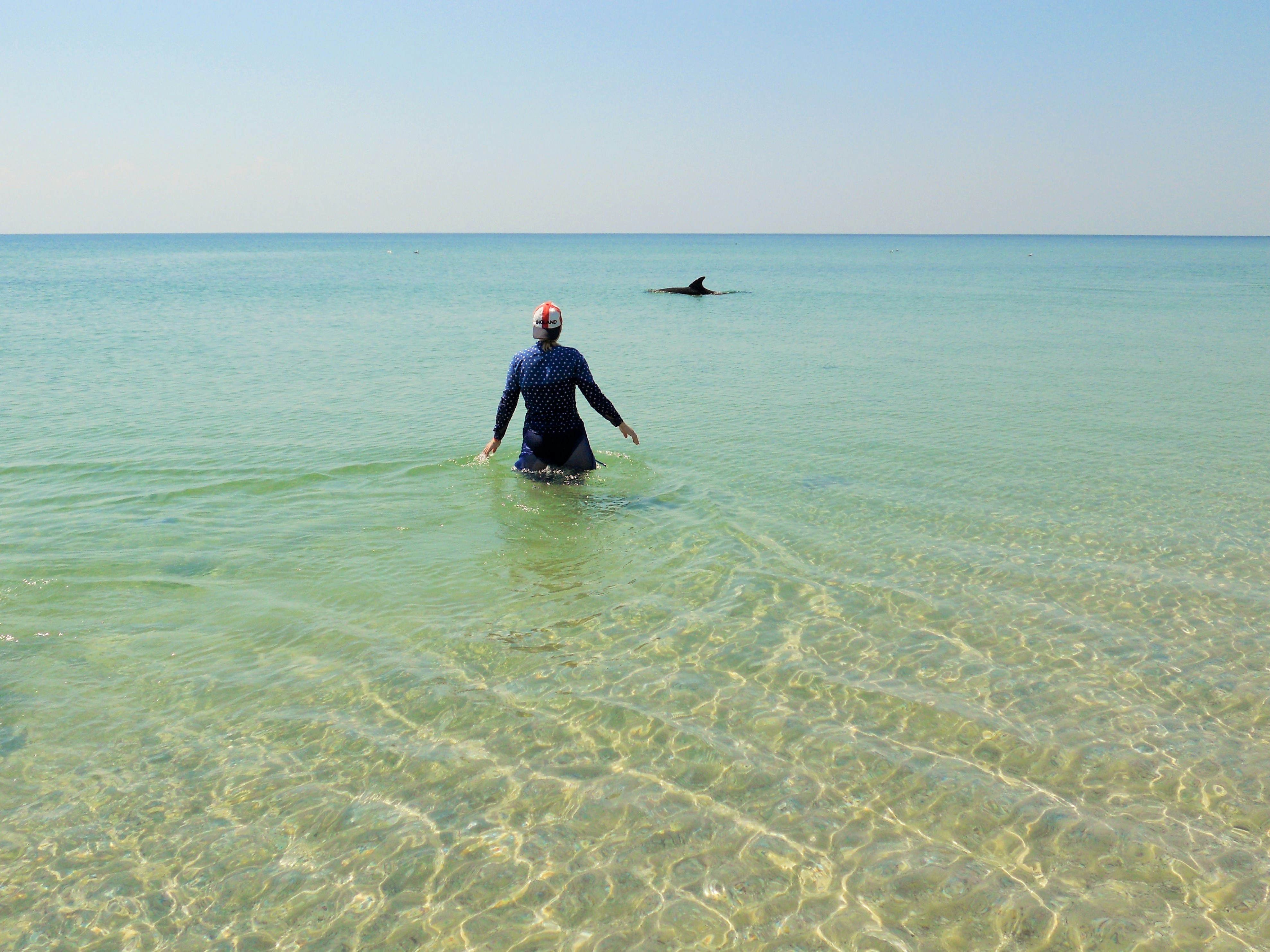 Solitary Swimmer in Crystal-Clear Tide Approaches a Distant Silhouette on the Horizon.