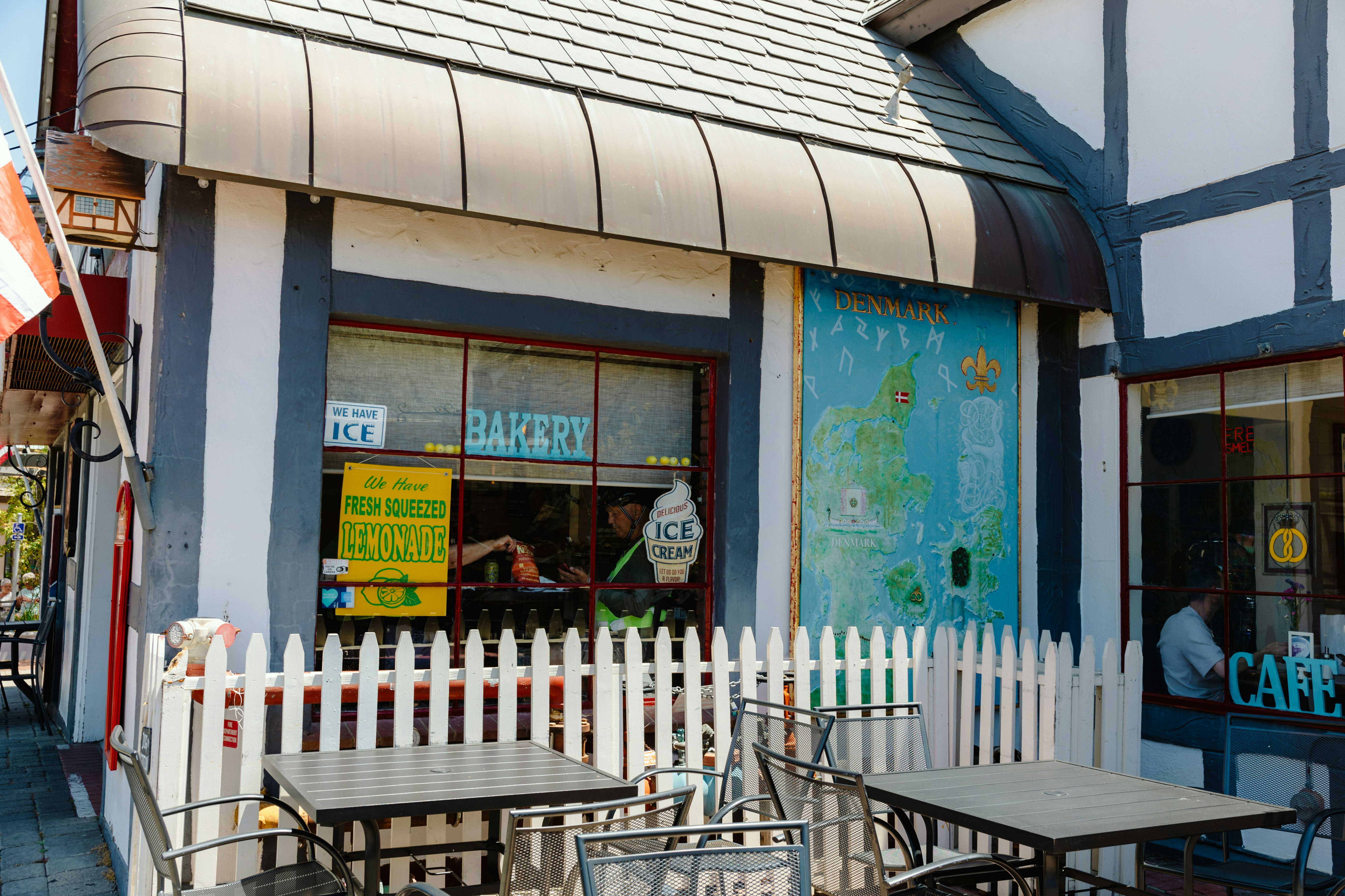 Sunlit Bakery Facade with Outdoor Seating and Picket Fence