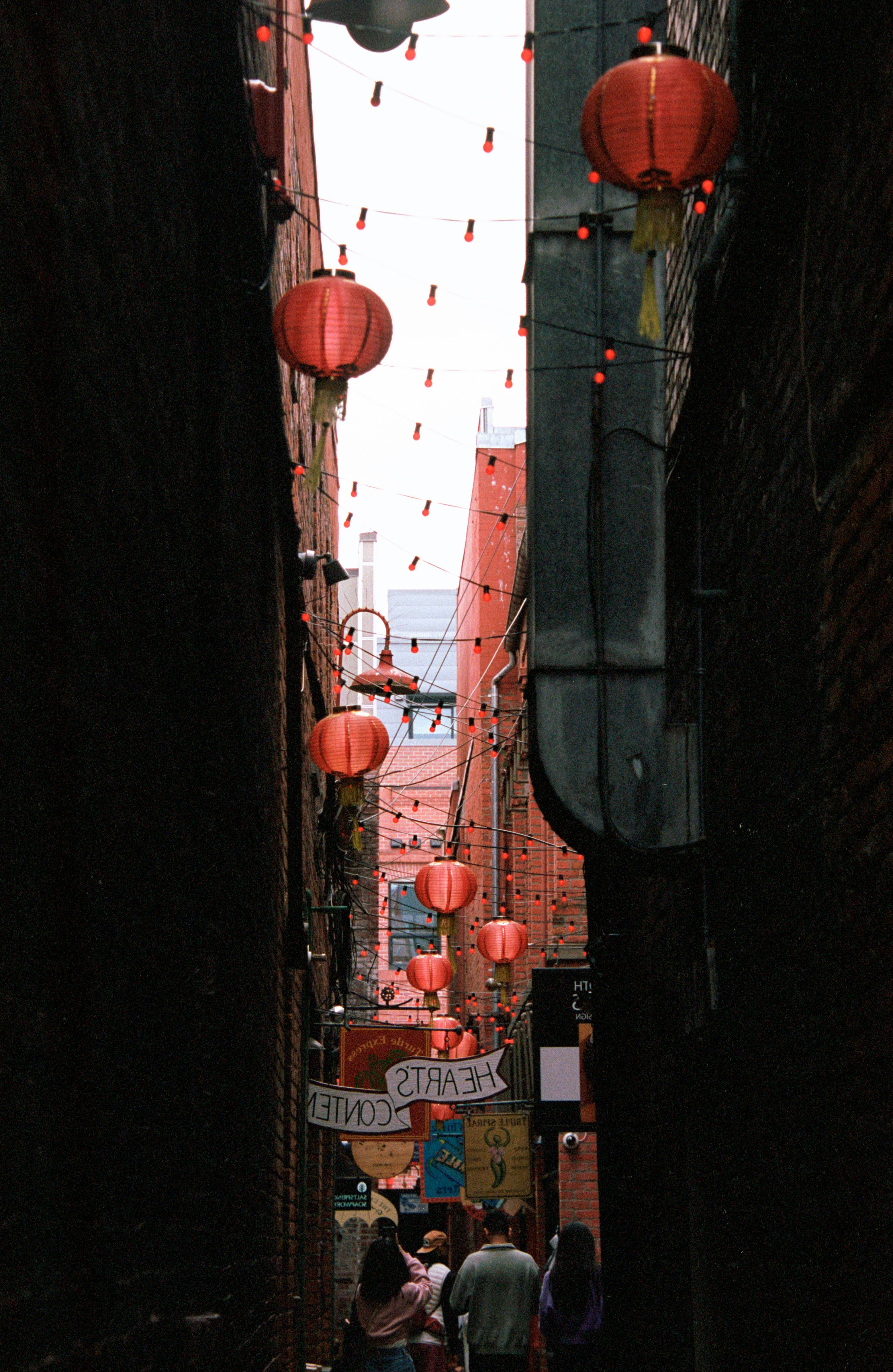 Narrow alley adorned with red lanterns and overhanging lights, creating a warm, inviting atmosphere.