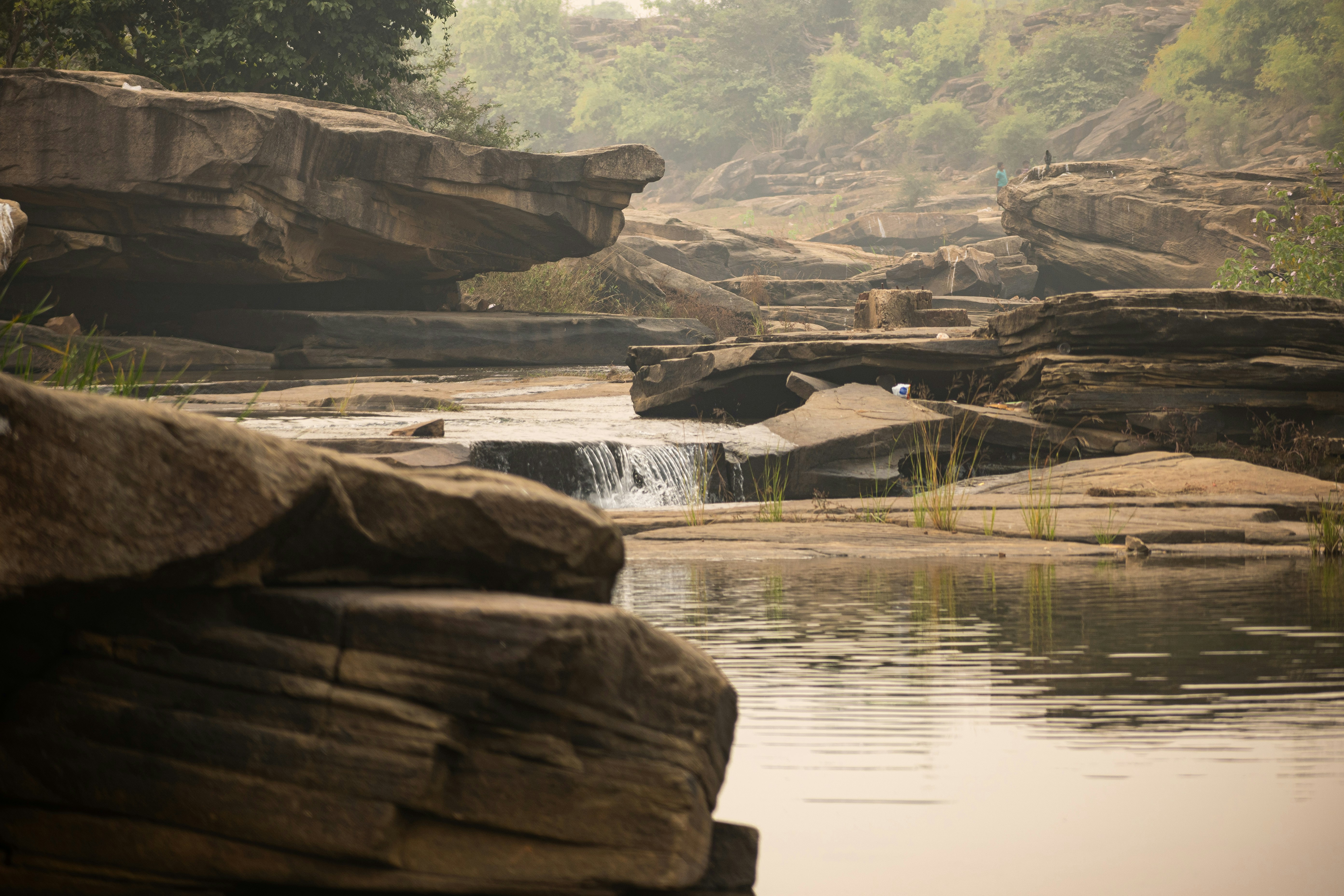 Gentle stream flowing through layered rock formations with lush greenery in the background.