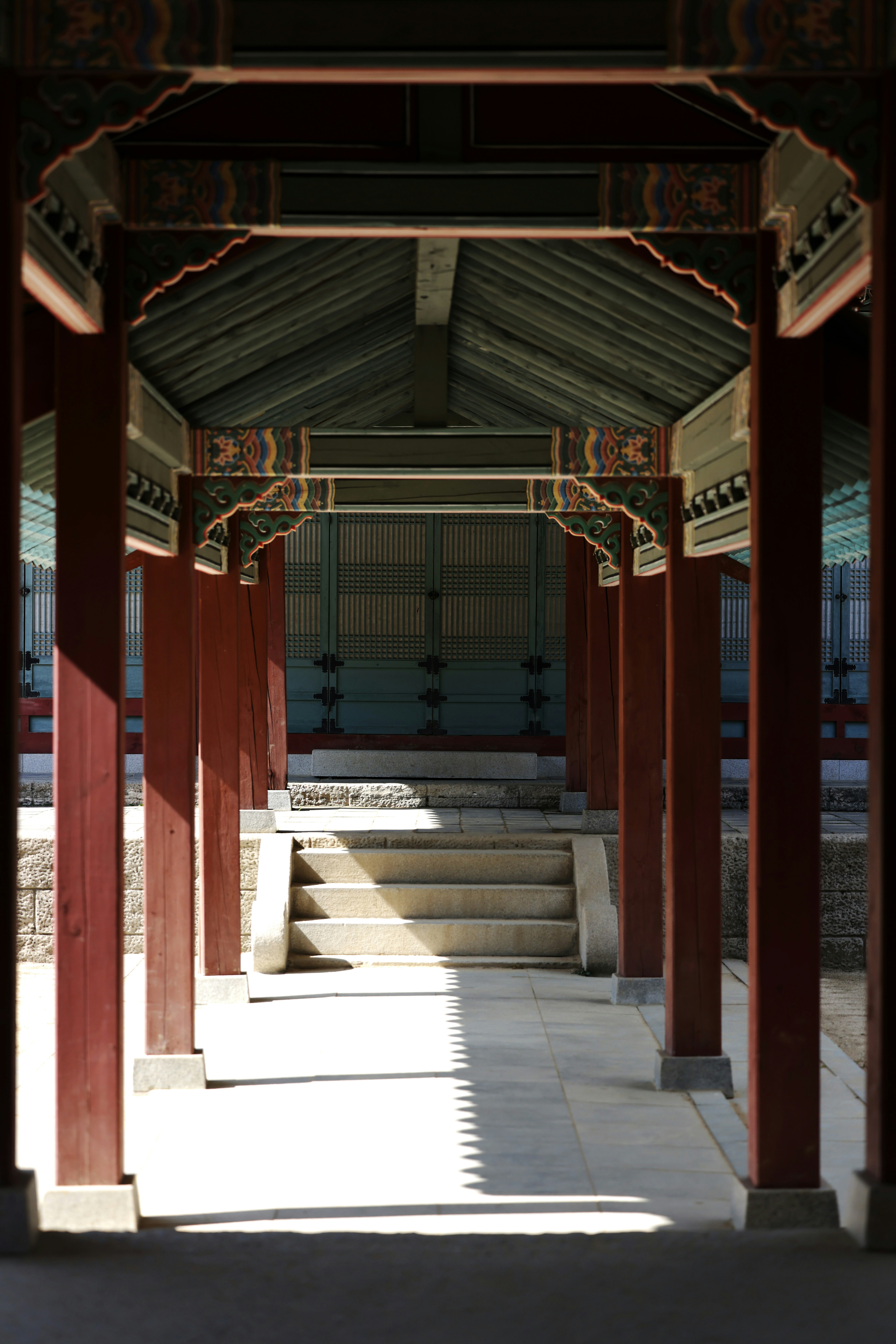A long walkway with red pillars leading to a building photo – Free ...