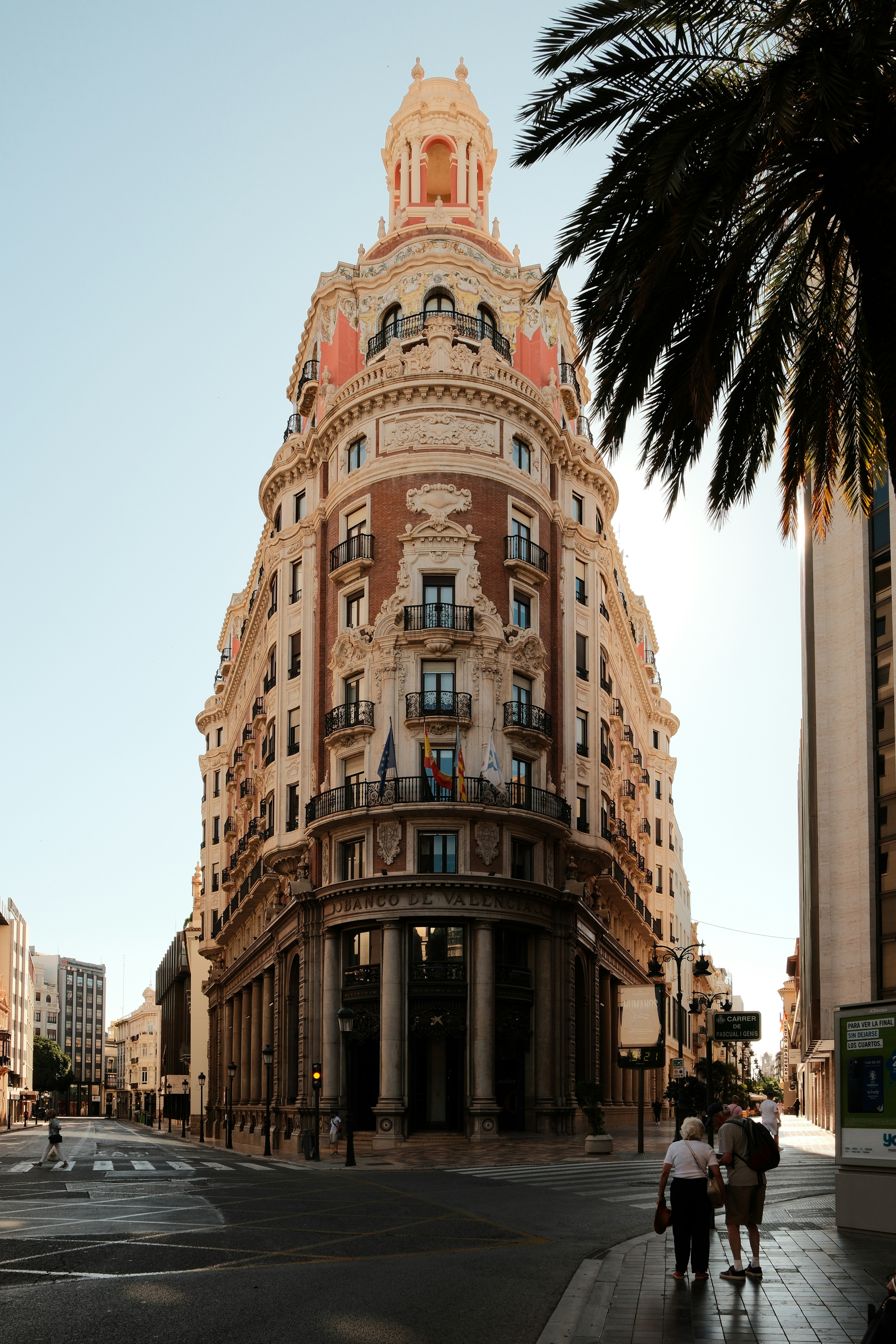 Historic building showcasing intricate architectural details on a sunlit street corner, with pedestrians strolling nearby.