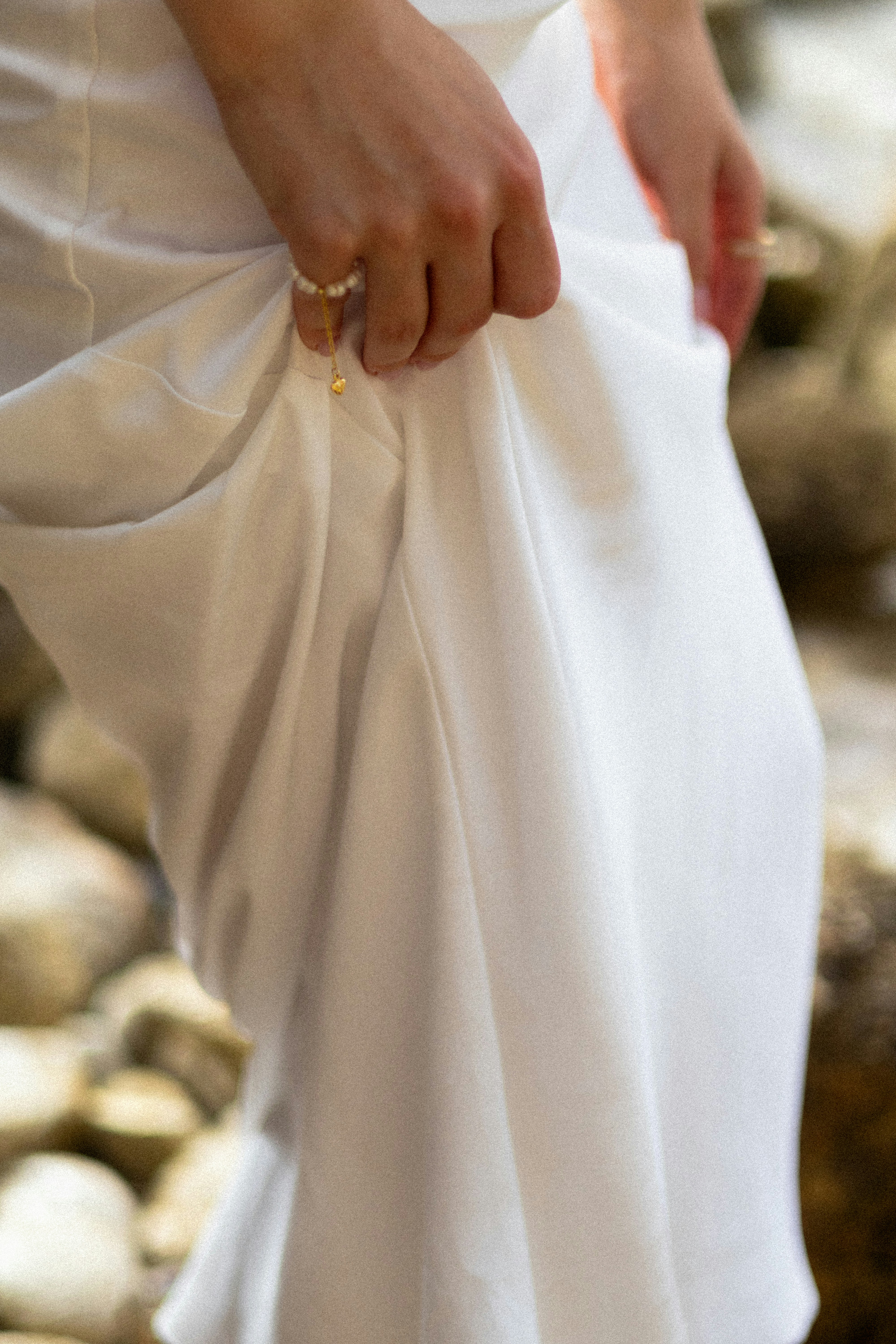 White gown drape and pocket detail at the edge of a rocky shoreline