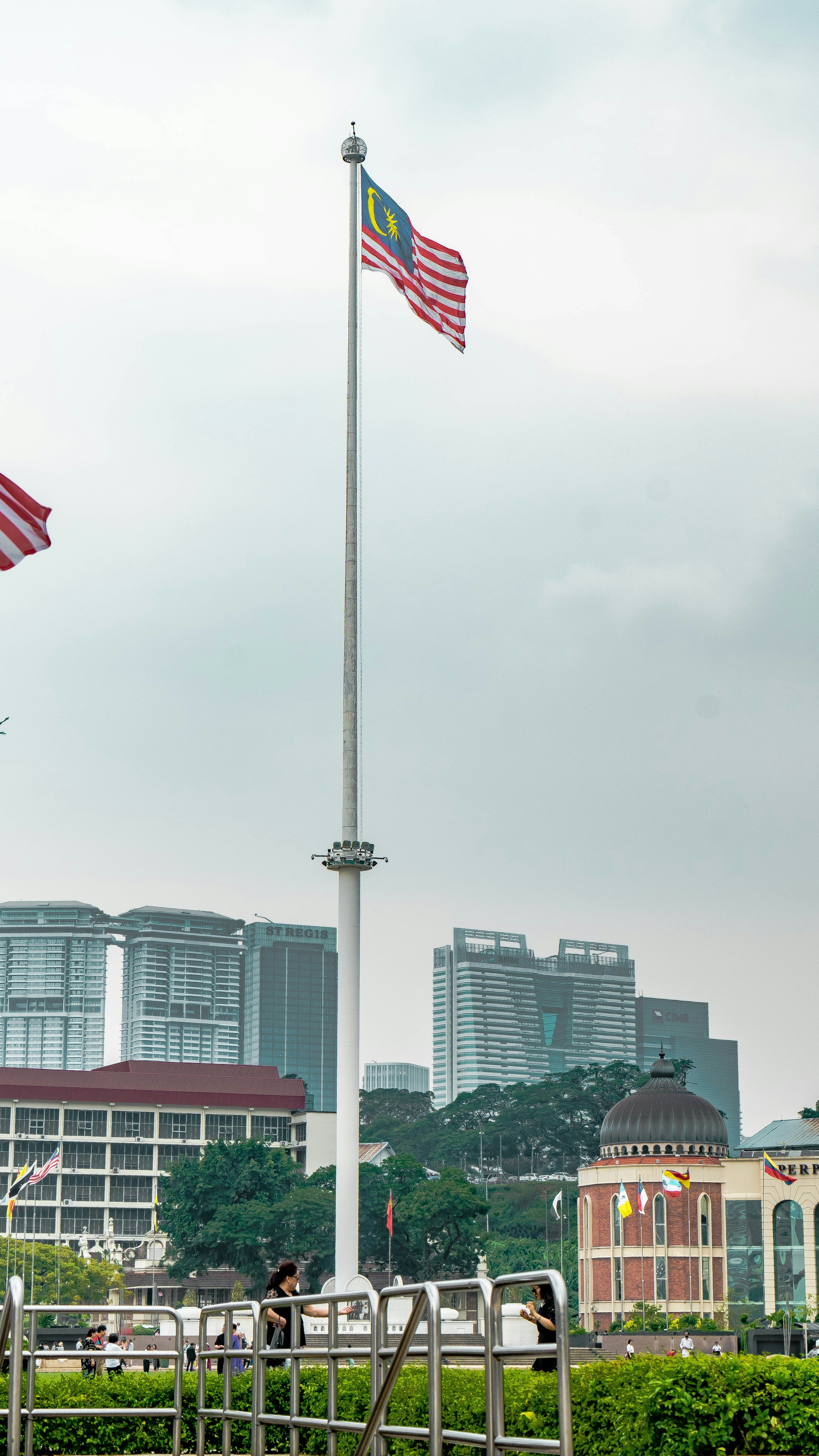 A Malaysian flag proudly flies above a bustling urban landscape, juxtaposed against modern skyscrapers and historical architecture.