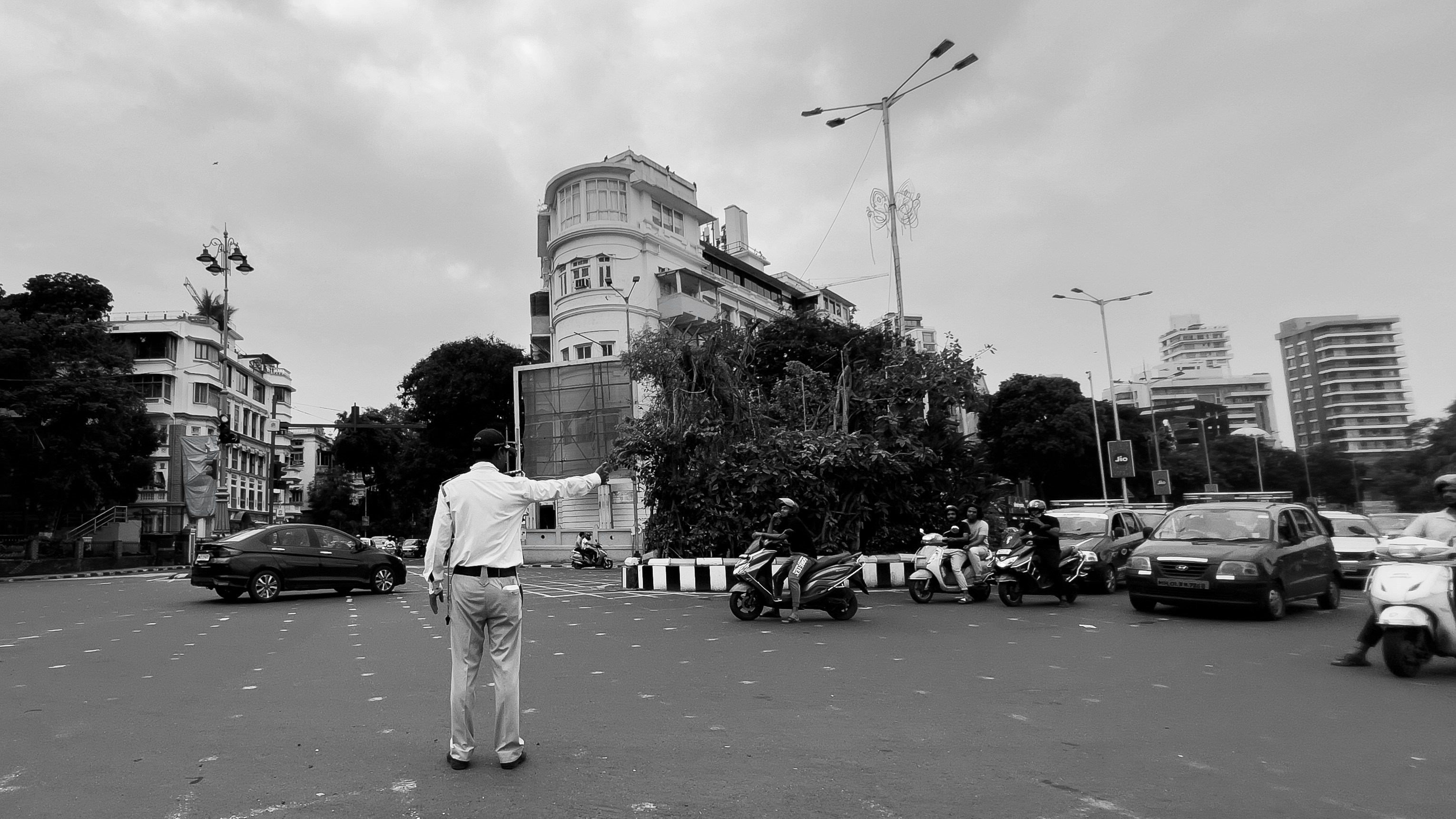 Monochrome scene of a bustling city intersection with a lone figure standing amidst traffic.