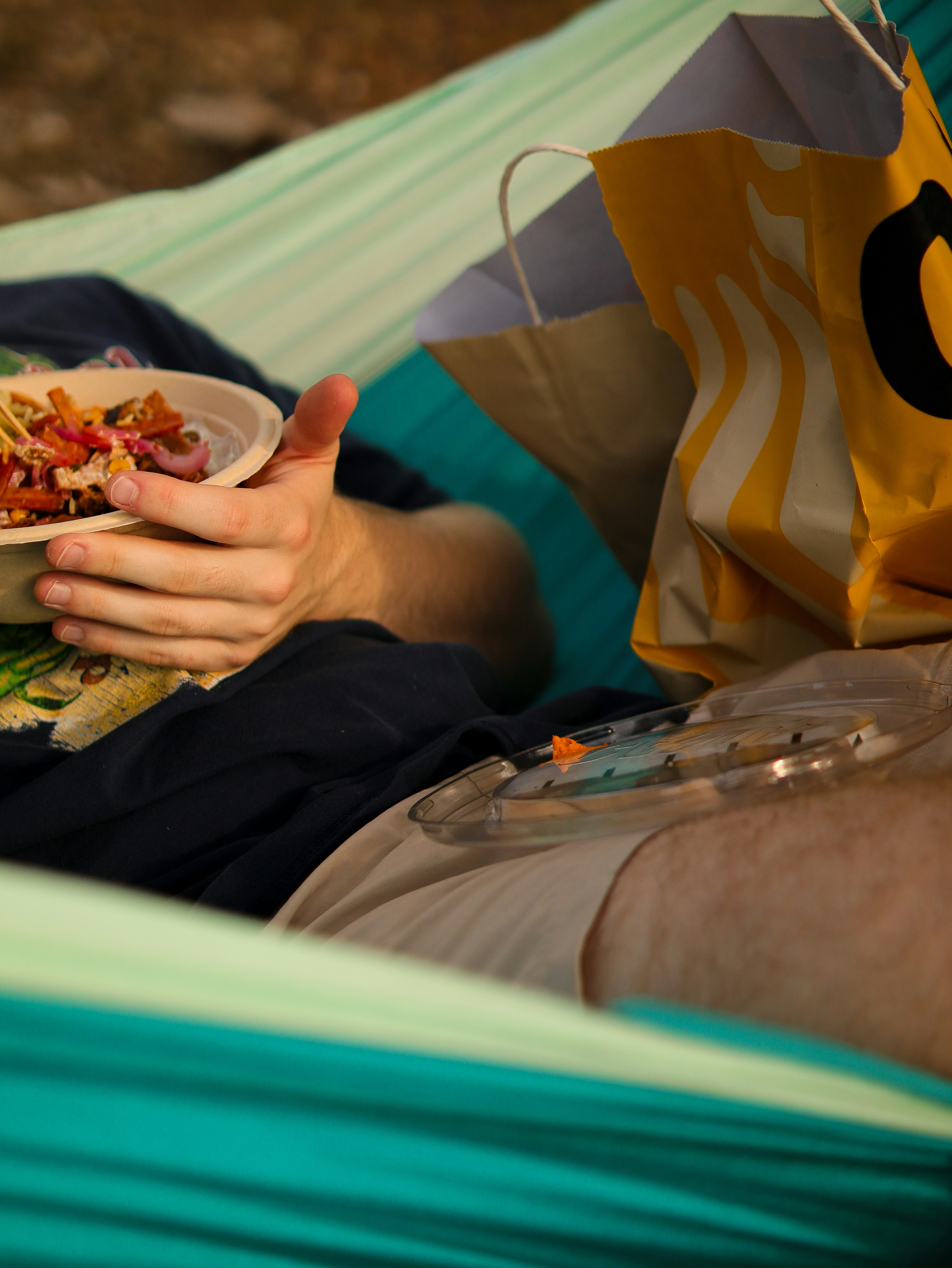 Casual picnic in a hammock: hands holding a bowl beside a yellow shopping bag