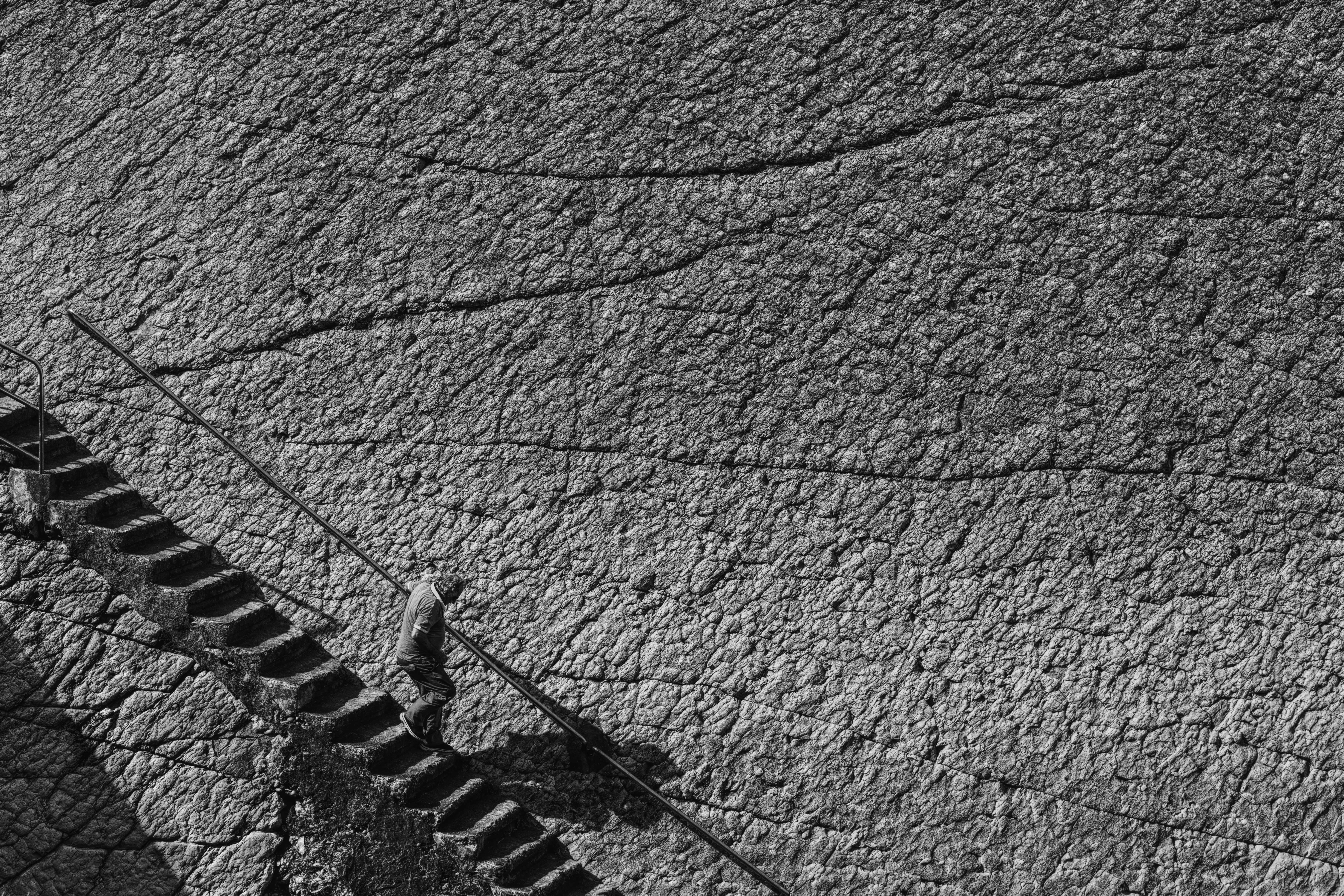 A solitary figure ascends a weathered staircase against a textured, cracked surface, highlighting the passage of time and human endeavor.