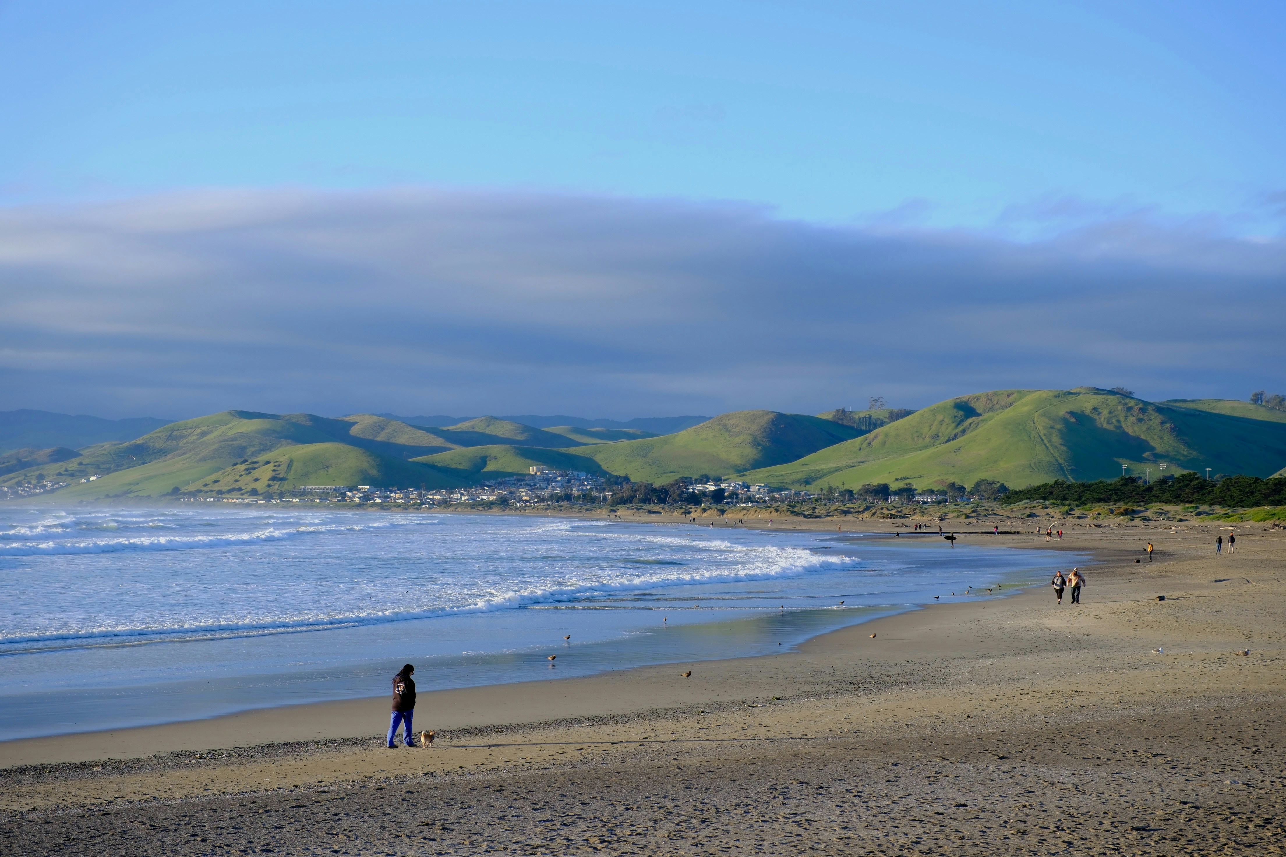 Lone Walker on a shoreline framed by emerald hills and Pacific blue waves