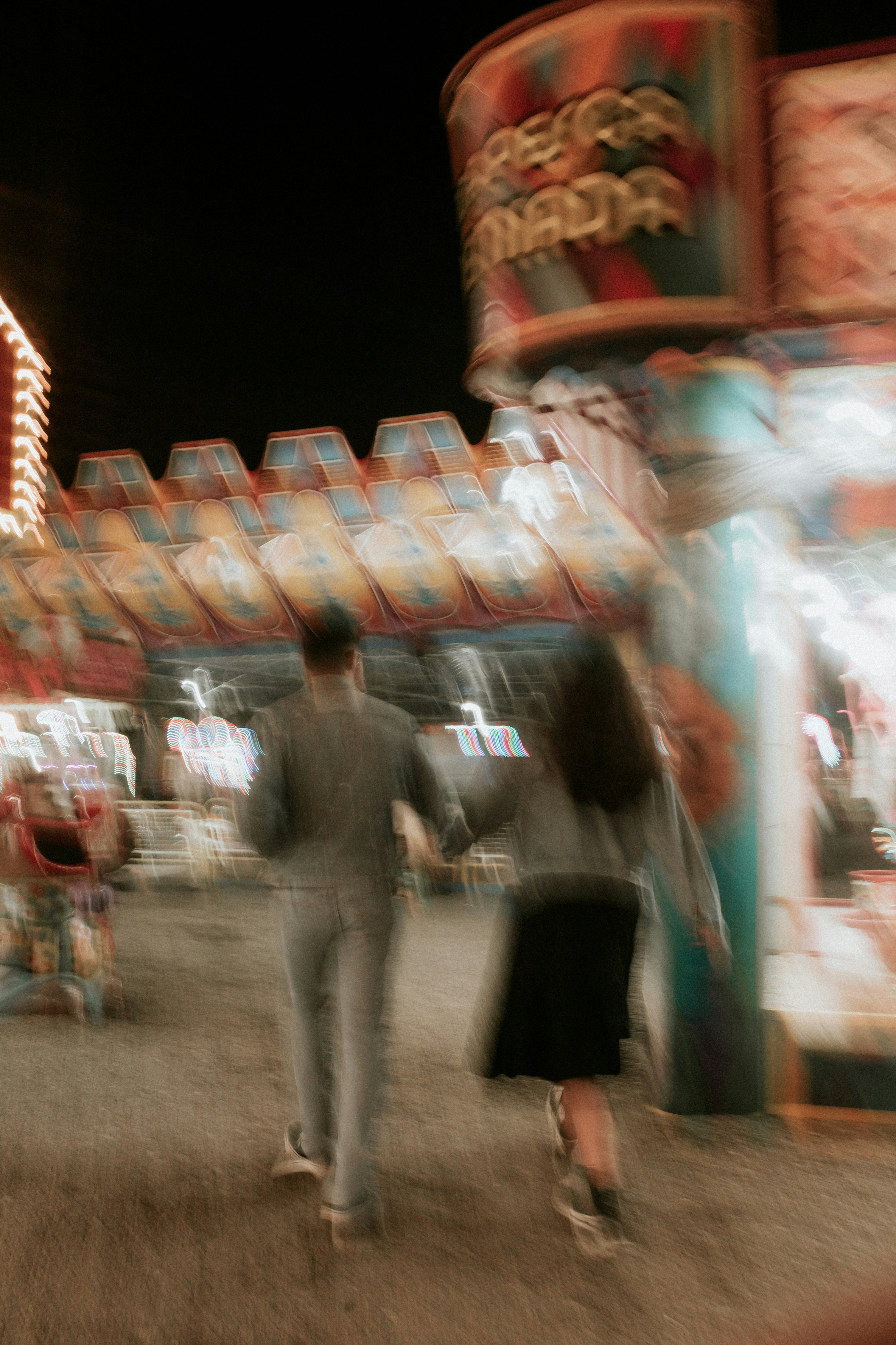 Neon Whirl: Two Figures Fade Through a Blurred Carnival Night