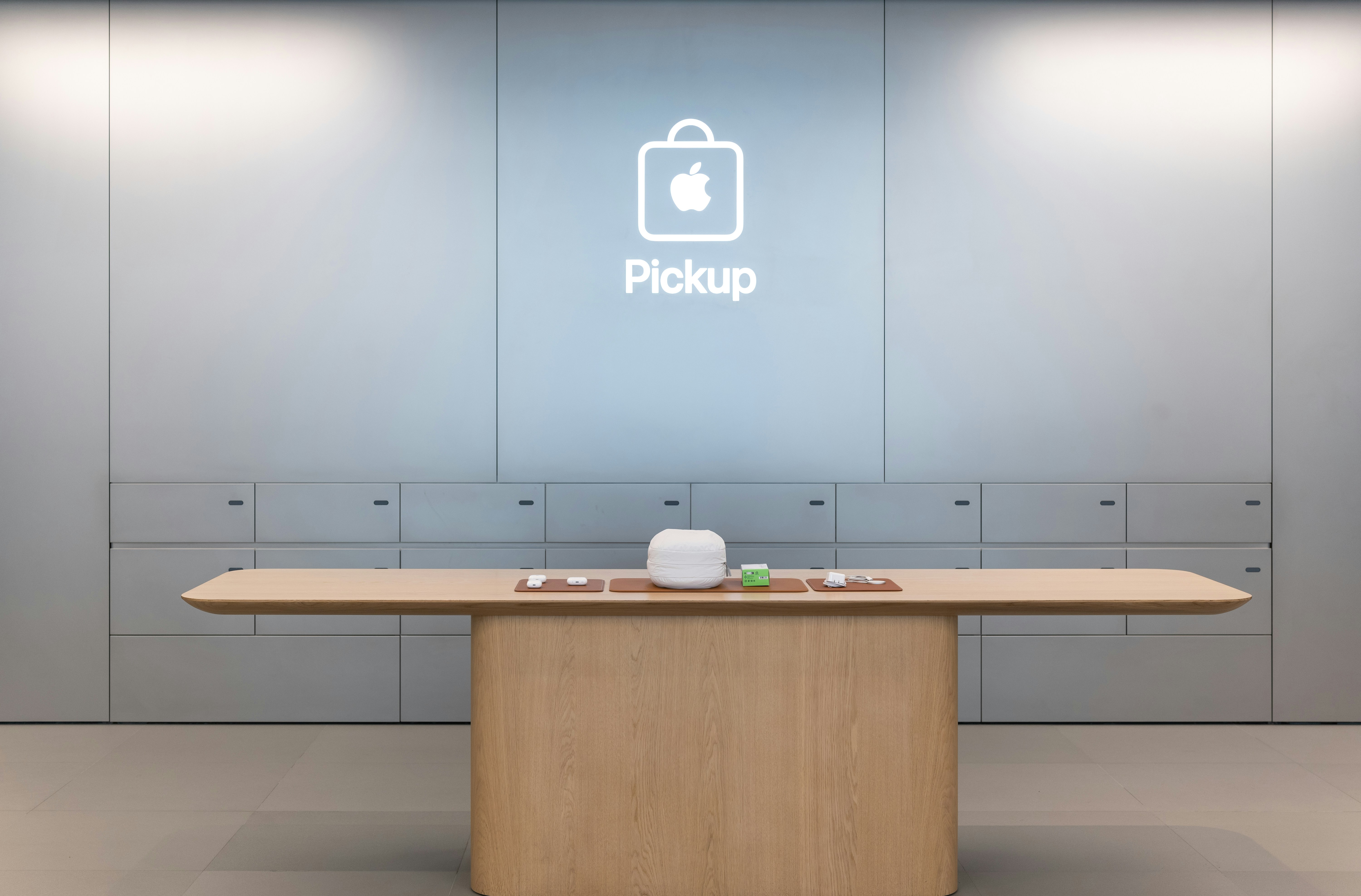 Minimalist pickup counter in a modern space, featuring a long wooden table and a grey wall with an illuminated Pickup logo.