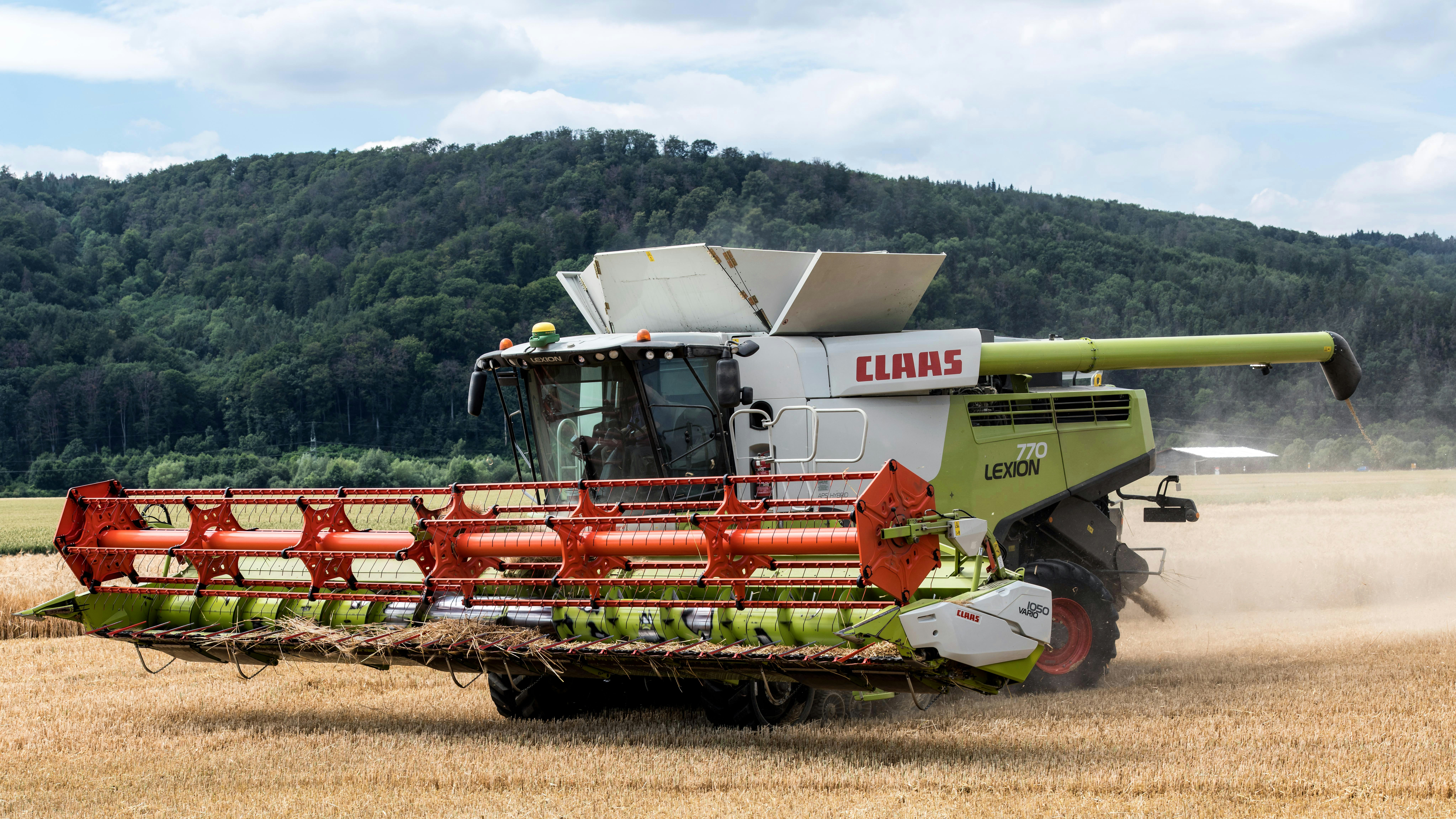 A green and white combine is in the middle of a field photo – Free ...