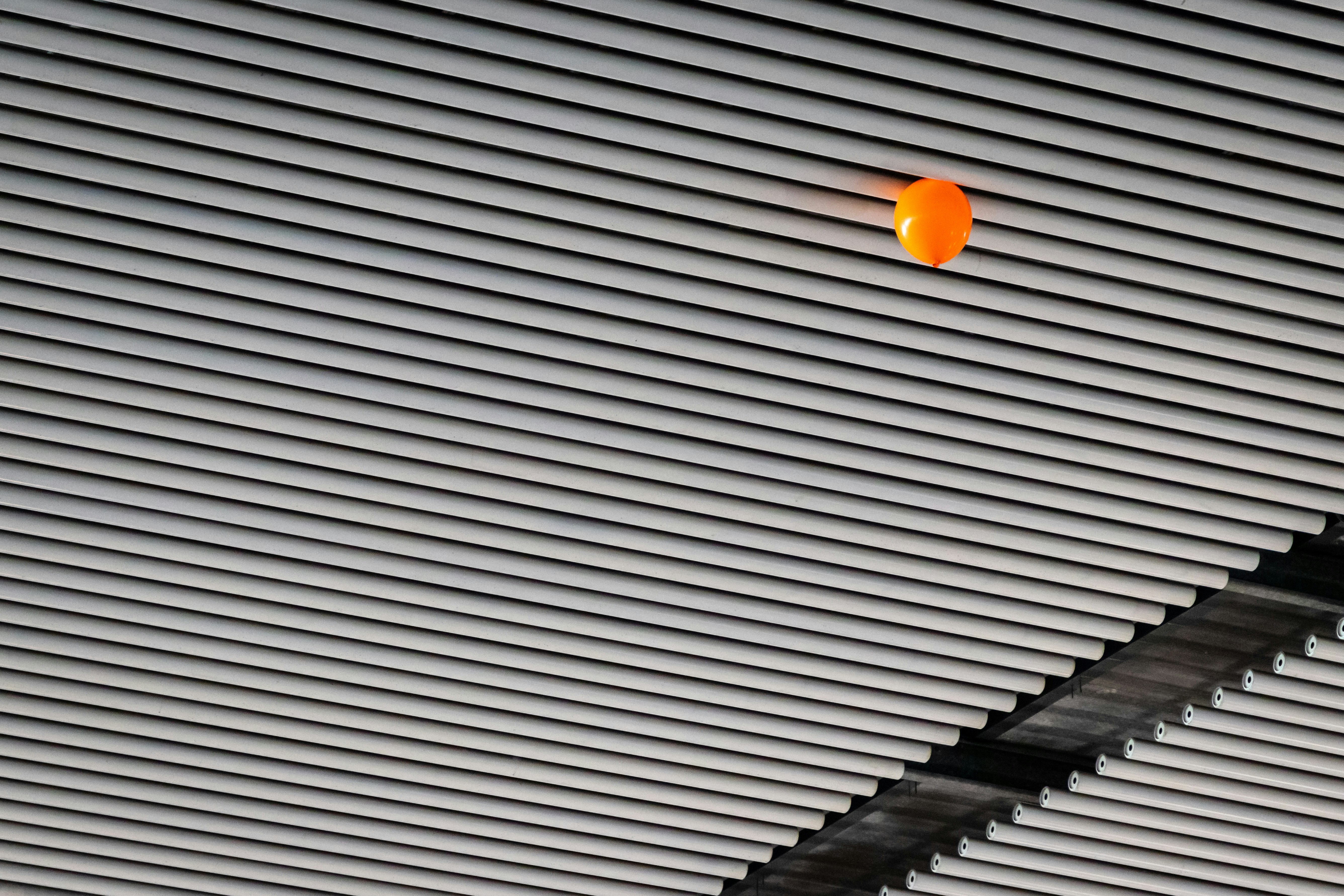 Amber Balloon Drifts Across a Facade of Parallel Louvers