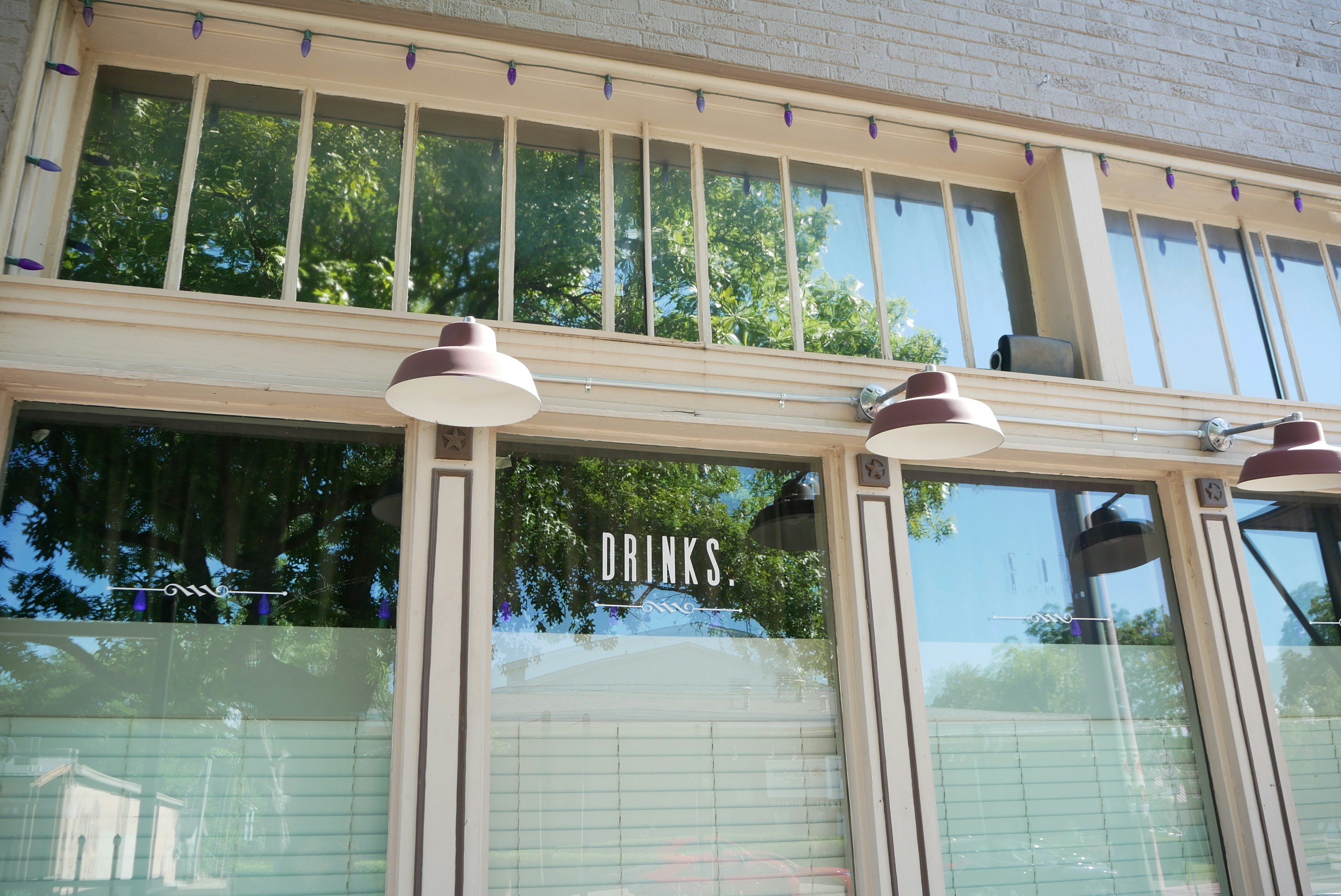 Sunlit Glass-Facade Café: Centered 'DRINKS' Sign Framed by Lamps