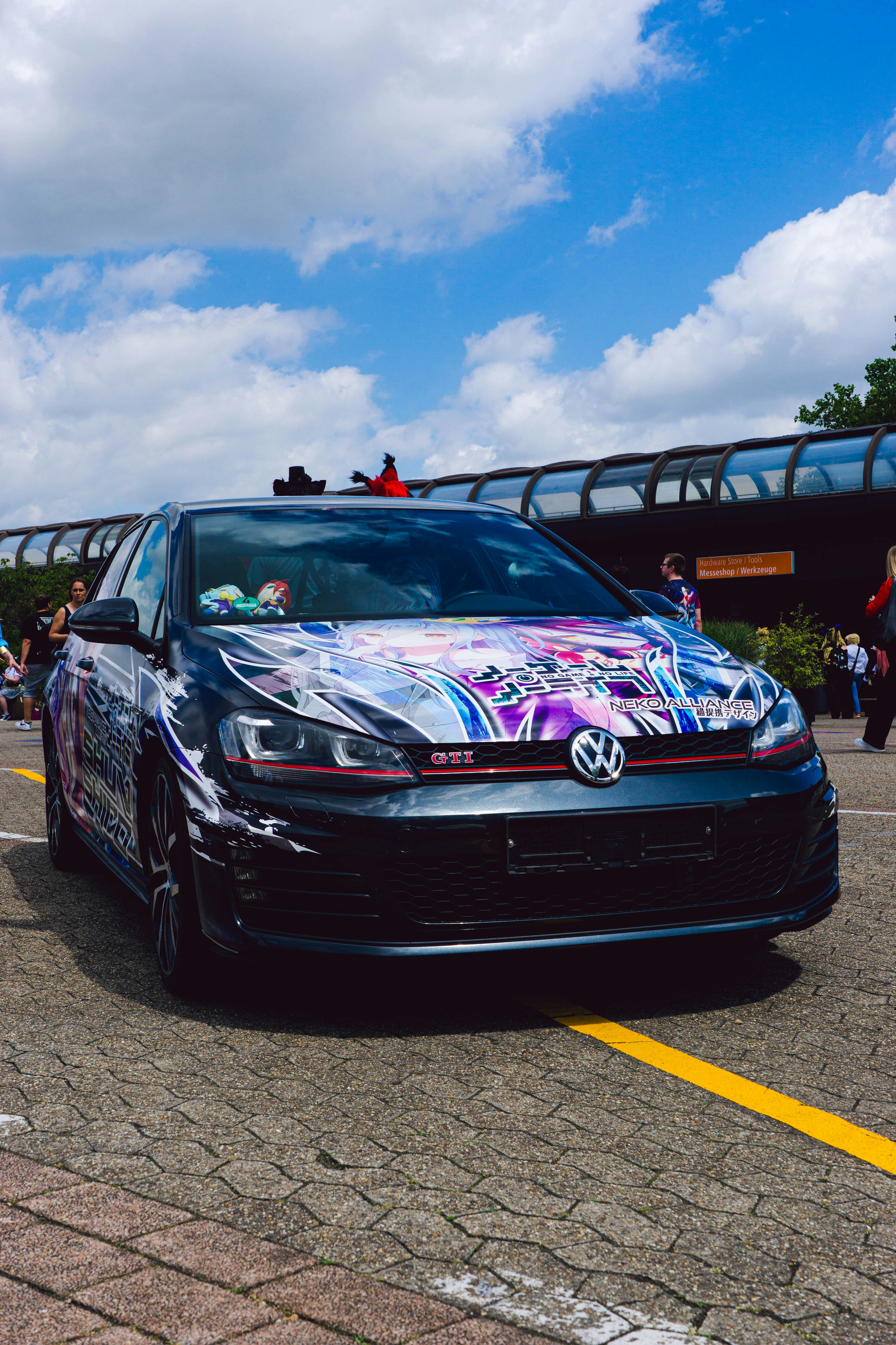 Volkswagen GTI adorned with eye-catching graphics, parked under a bright sky at a lively event.