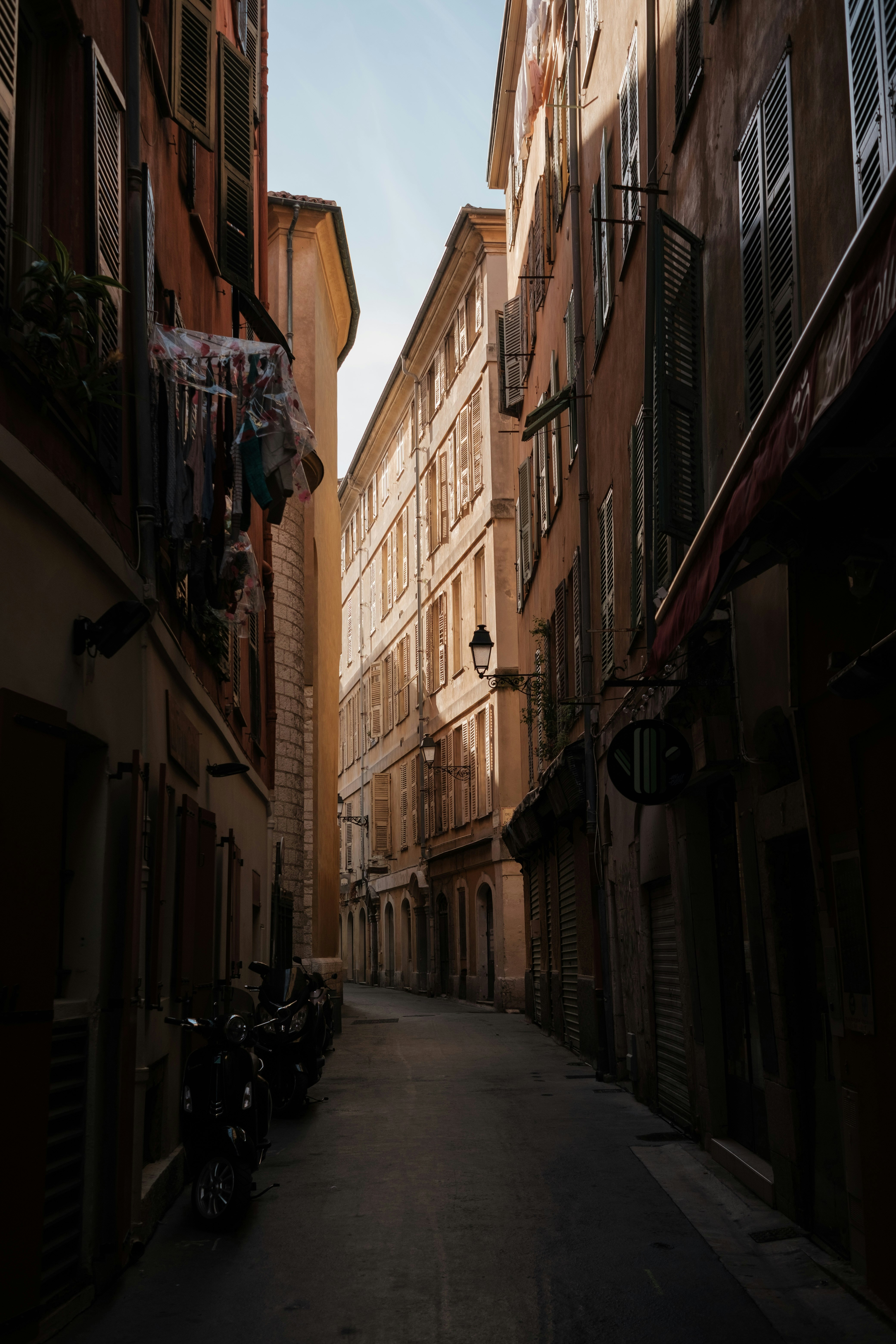 Narrow alleyway flanked by sunlit buildings and hanging laundry, evoking a sense of tranquility in a bustling city.