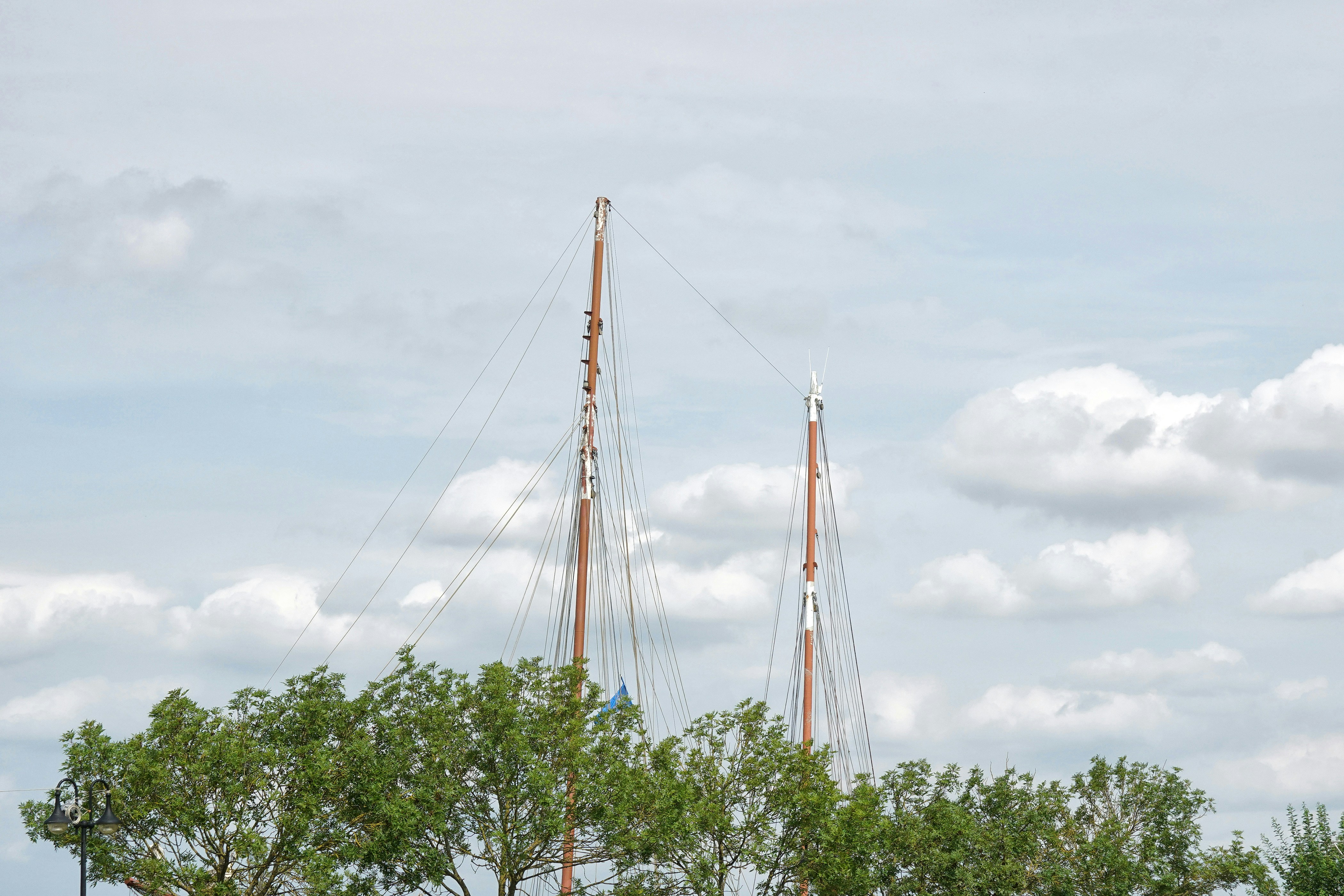 Sailboat masts rise above lush green trees under a partly cloudy sky.
