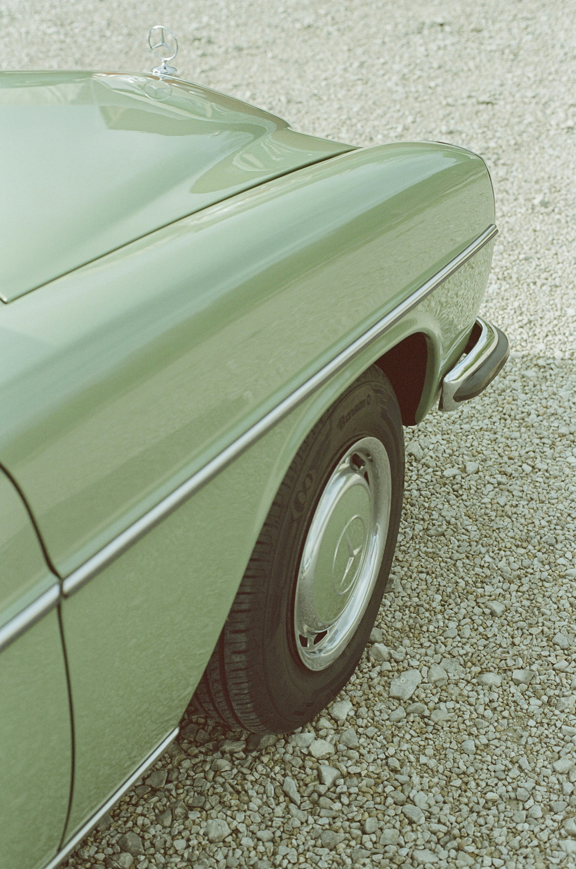 Close-up of a vintage green Mercedes car's front wheel and fender on a gravel surface.