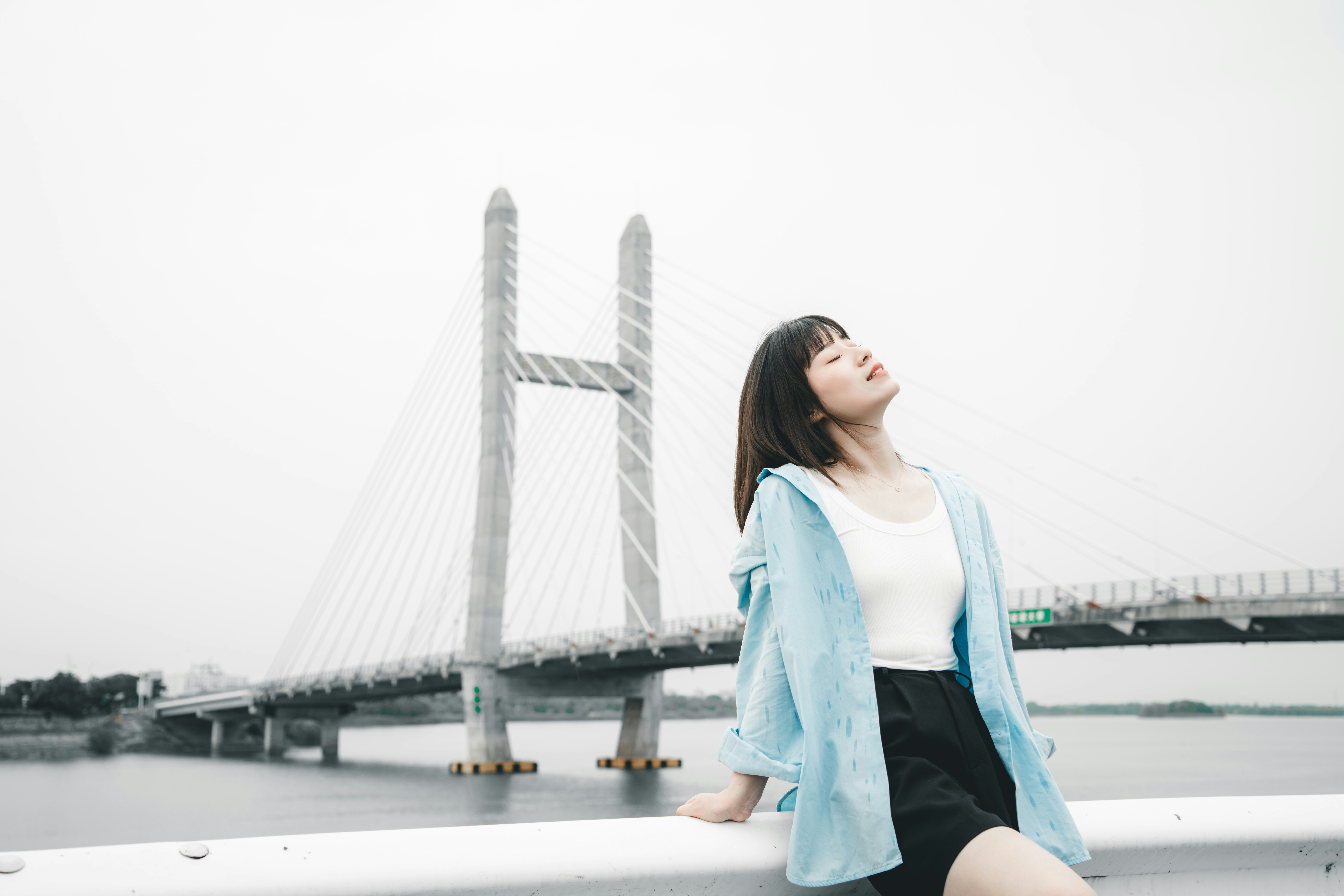 A woman leaning on a railing with a bridge in the background photo ...