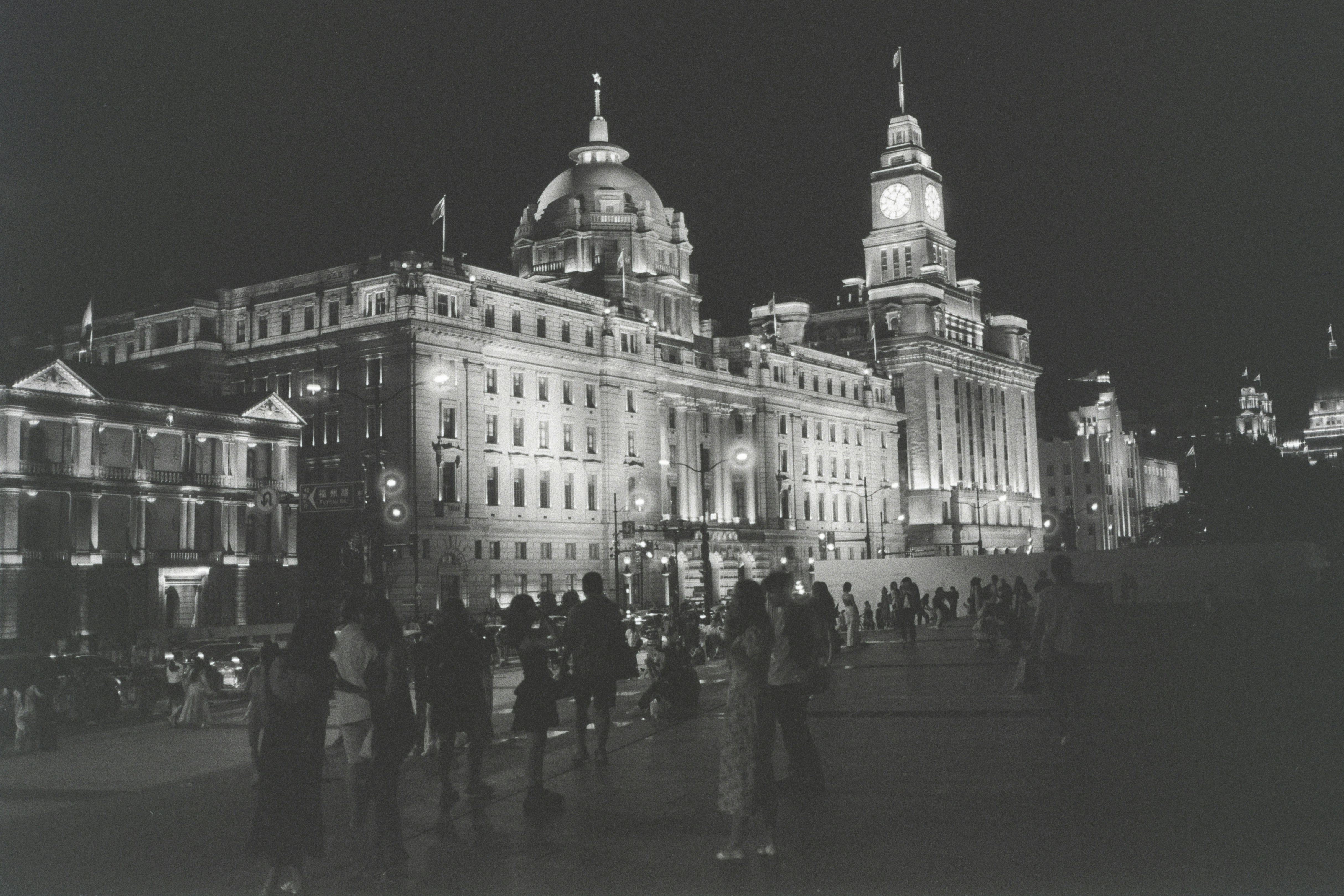 Historic buildings glow against the night sky as silhouettes of people gather below.