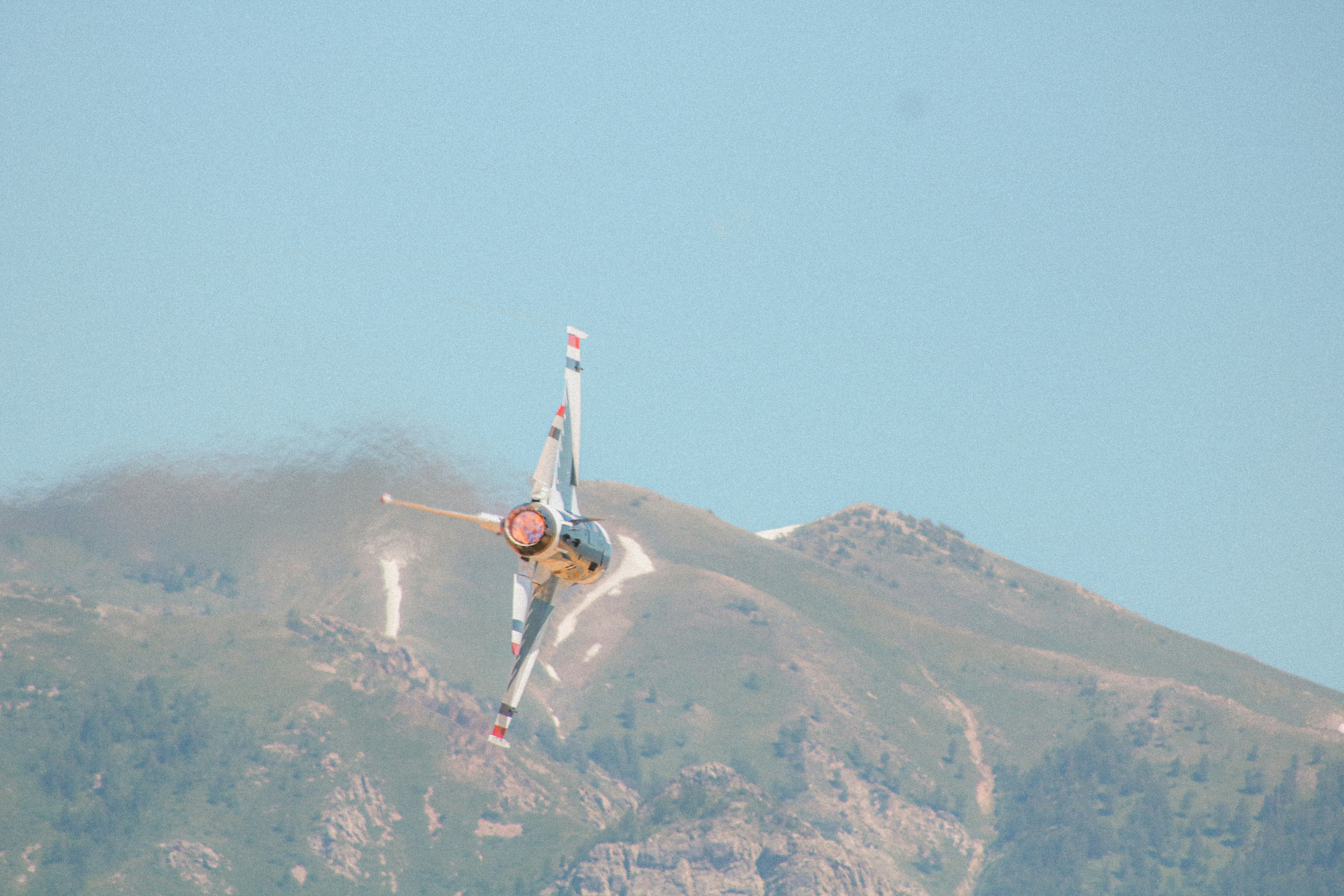 Alpine Aerial: Red-and-White Stunt Plane Carving a Diagonal Arc Over Granite Ridge