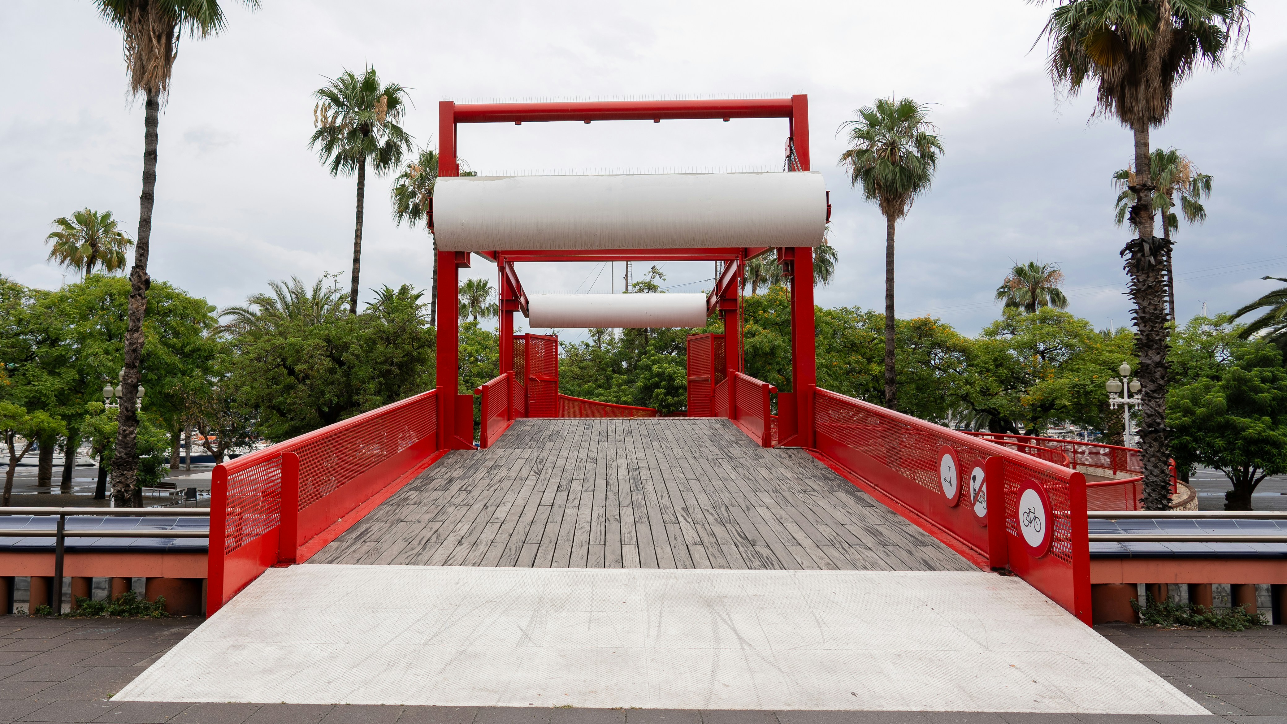 Scarlet Gateway: A Red Pedestrian Bridge Framing a Palm-Fringed Horizon