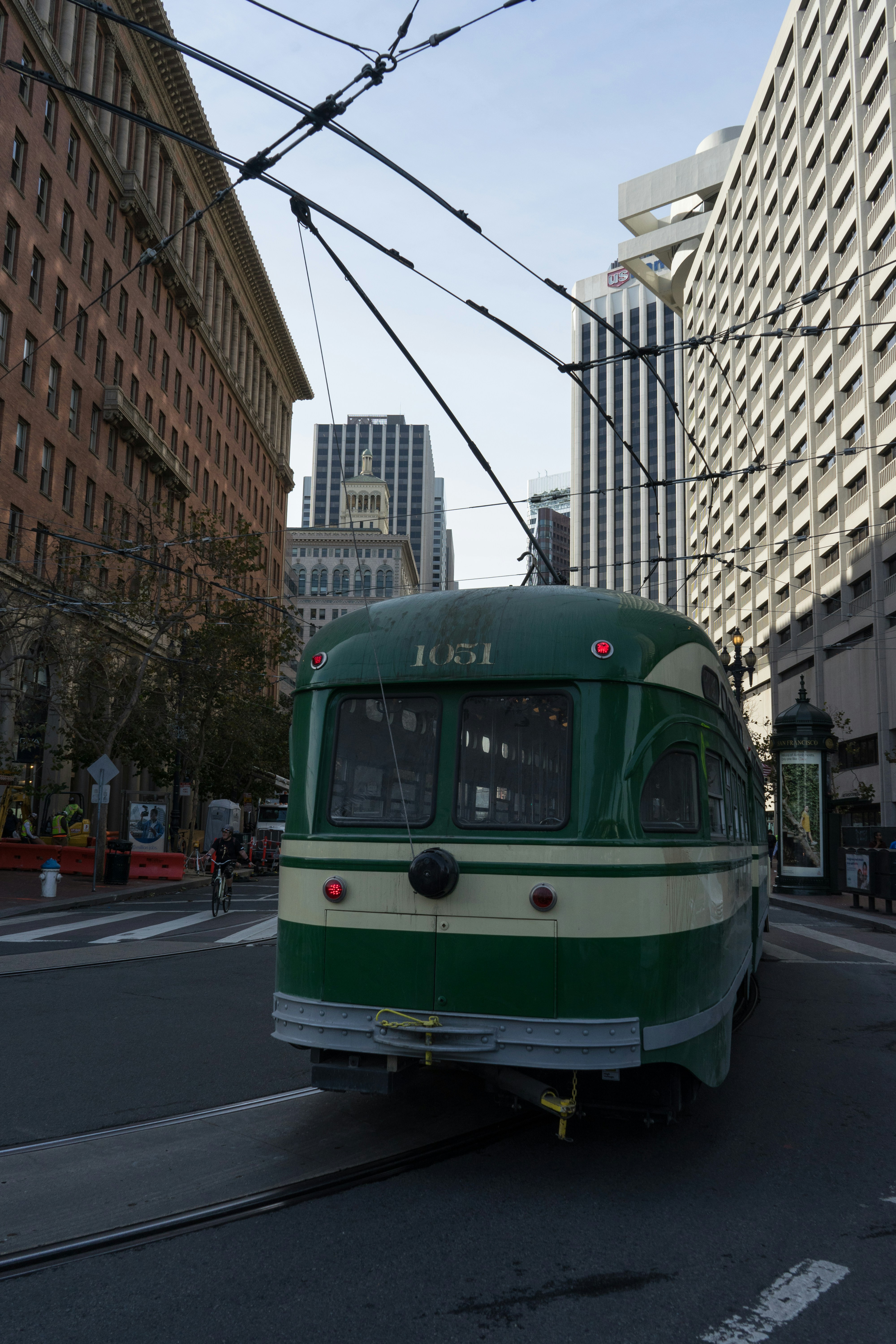 Green Streetcar Navigates a Concrete Canyon Under a Web of Overhead Wires