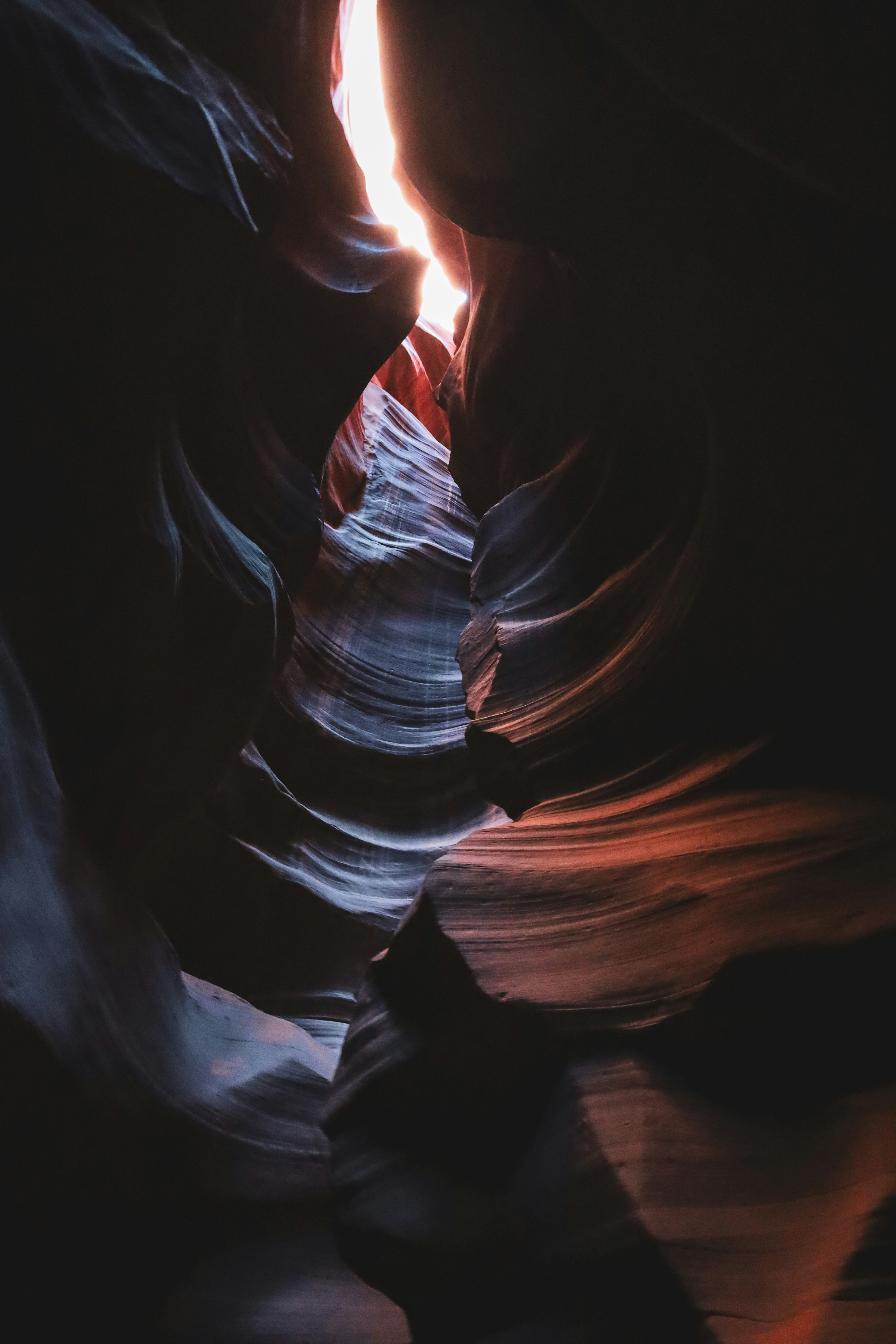 Sunlight filters through the narrow crevices of a sandstone canyon, highlighting the smooth, wavy textures of the rock formations.